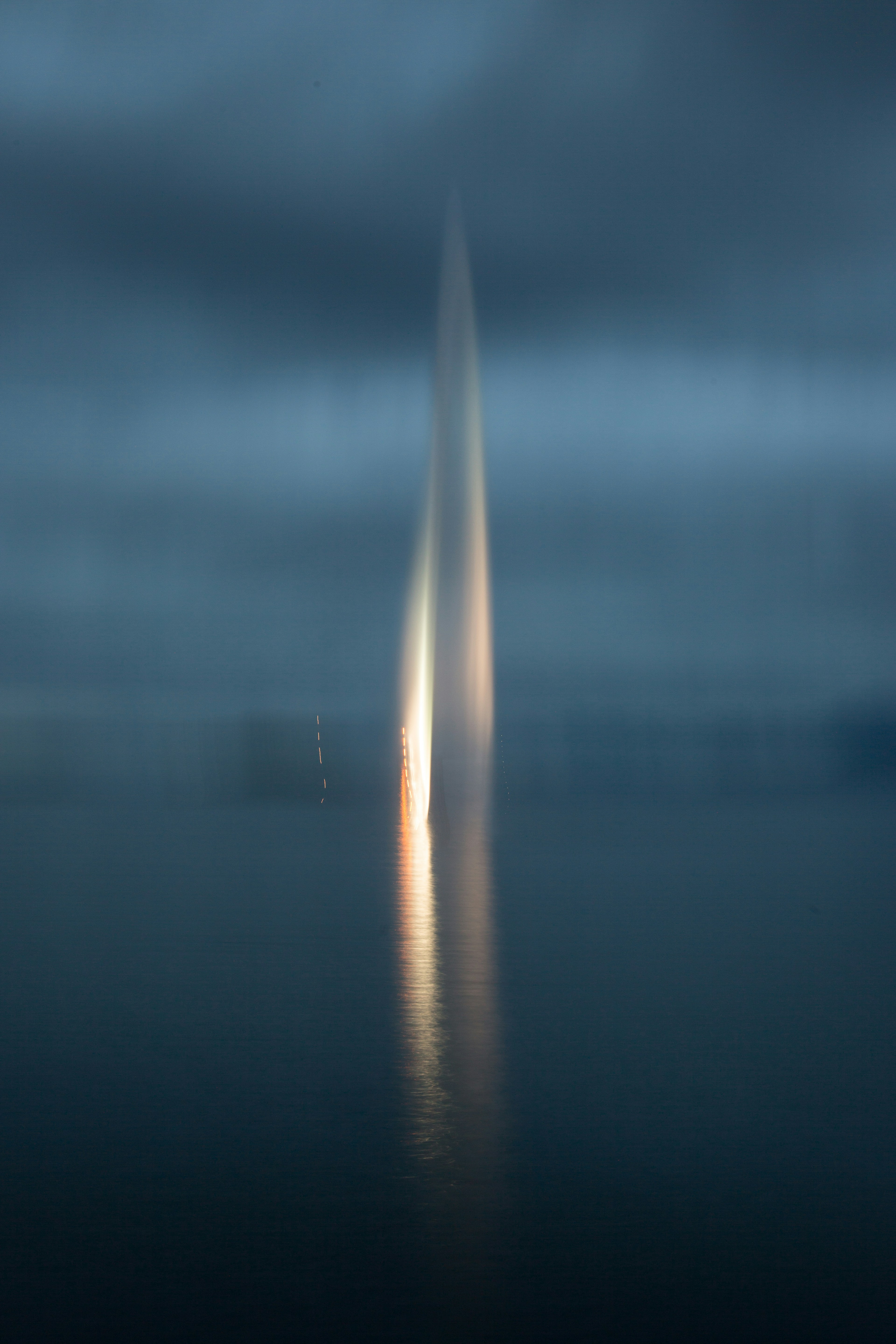 Vertical blaze: a lone rocket of light rising from calm seas