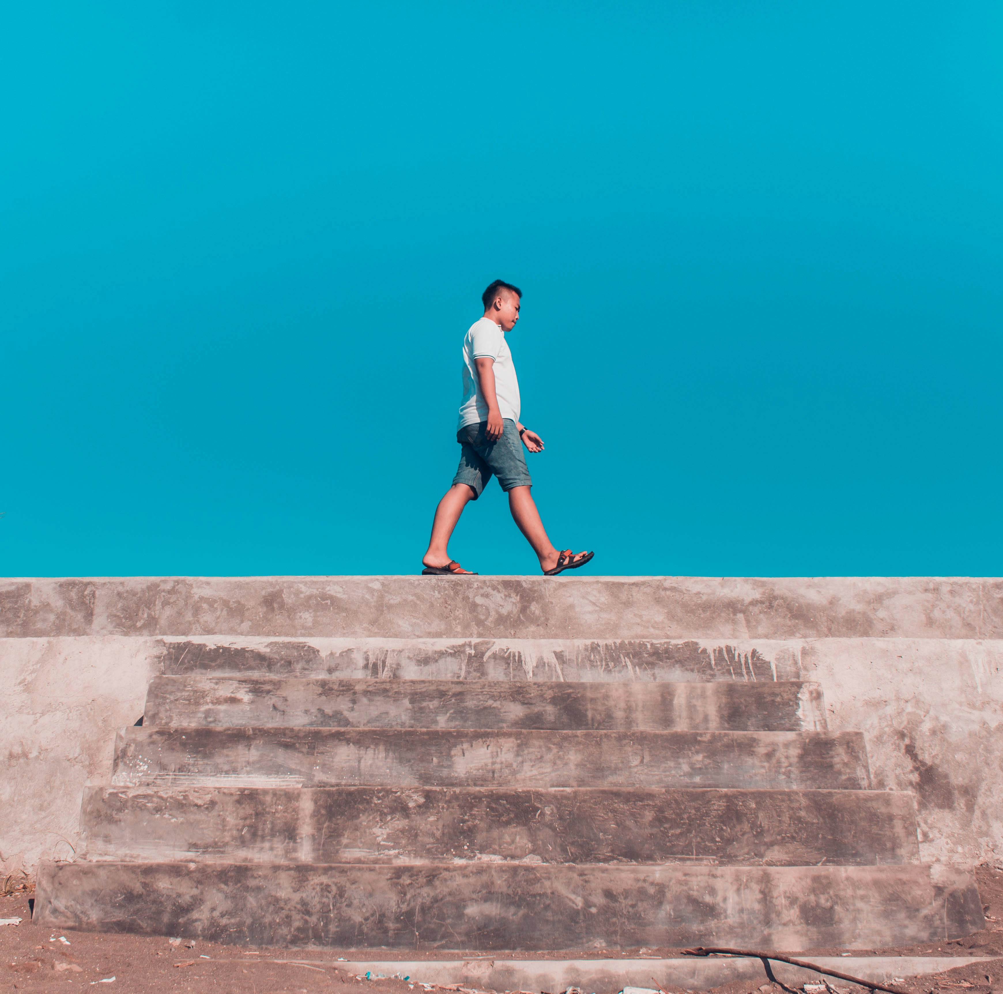 Azure Summit Stroll: A lone traveler strides along sunlit steps beneath a vast blue sky