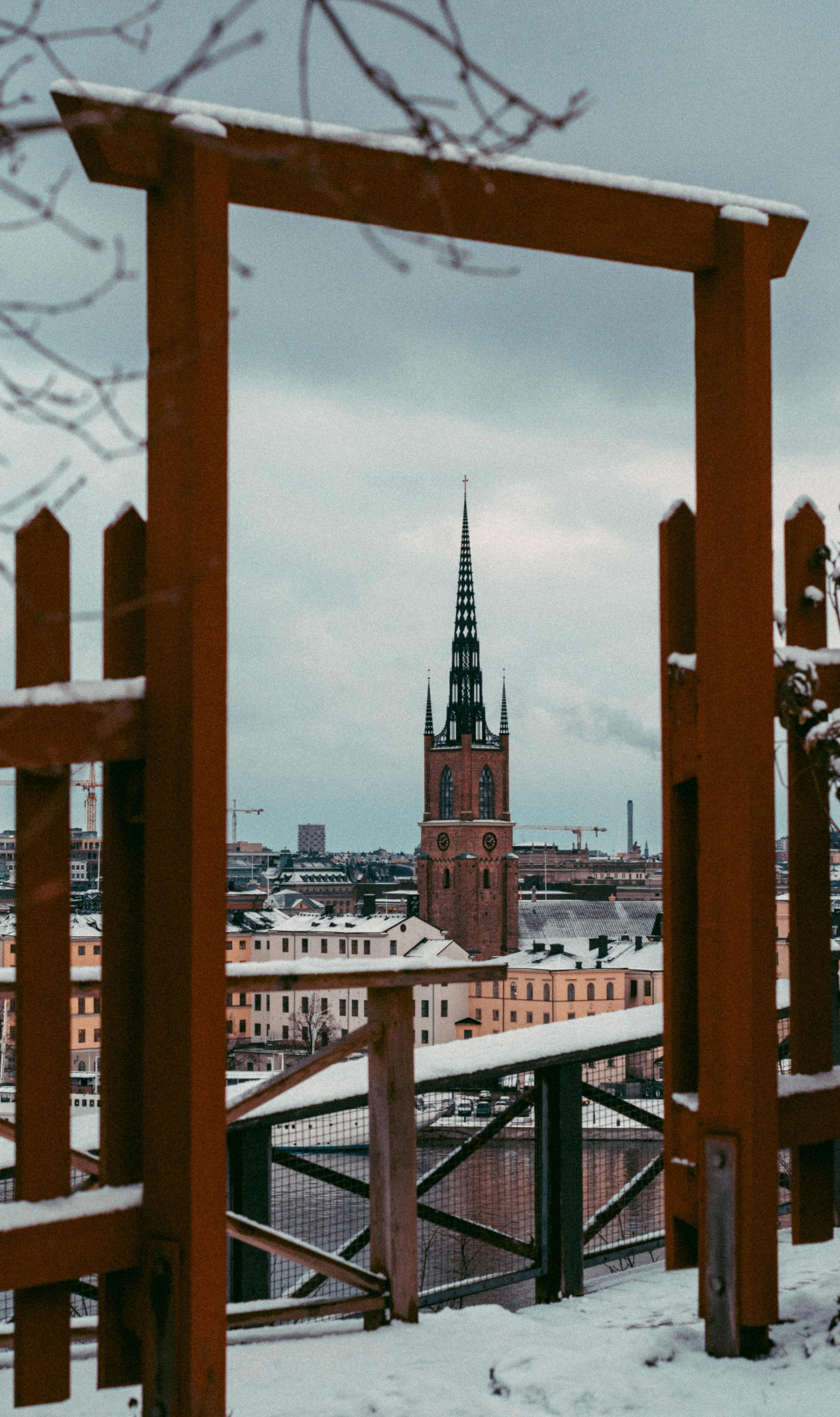 Historic church spire rises above a snow-covered cityscape, framed by a wooden gate. The scene captures the serene beauty of winter architecture.