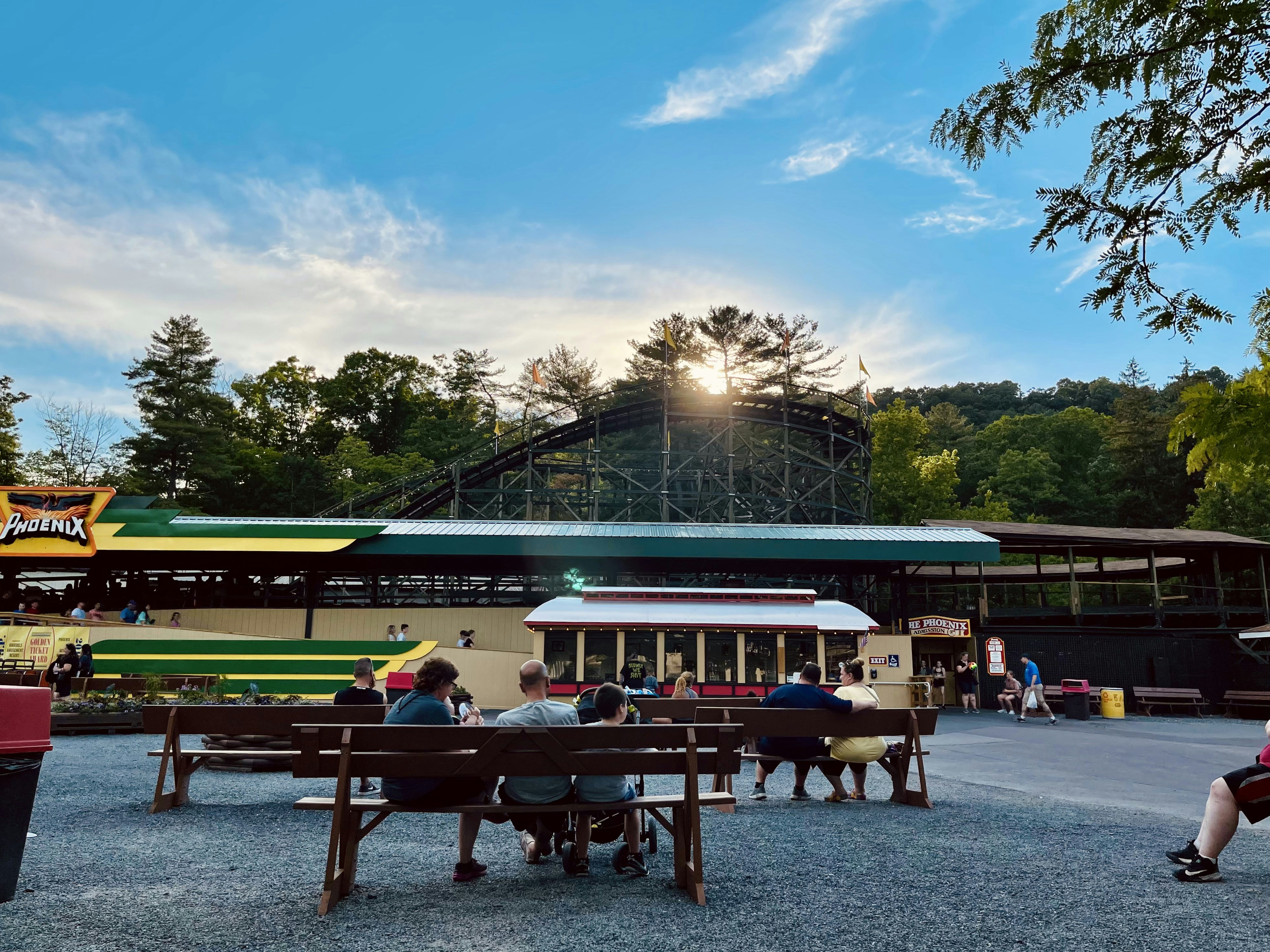 a group of people sitting at picnic tables in front of a roller coaster