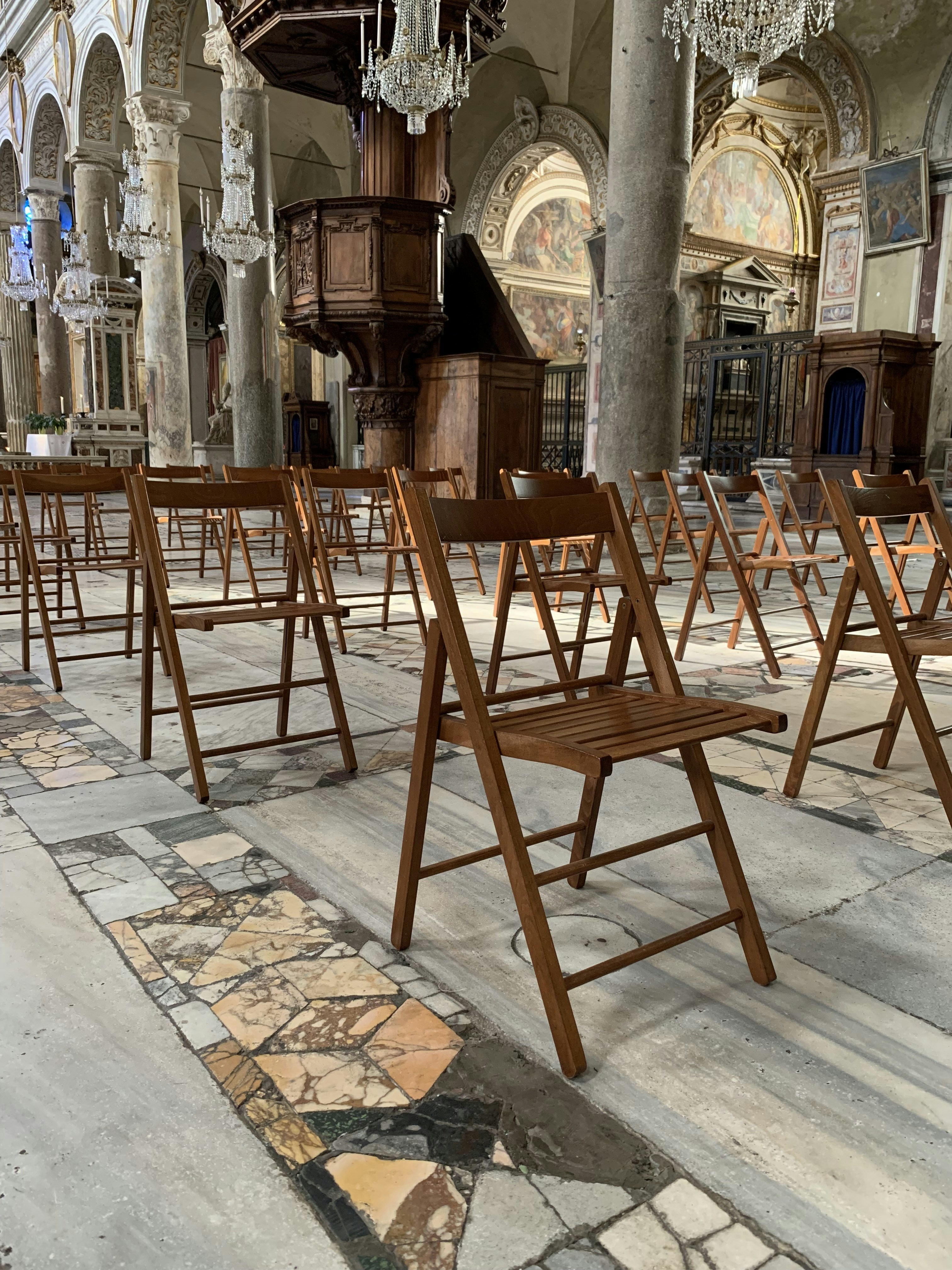 Empty wooden chairs arranged in a historic interior, showcasing intricate architectural details and serene ambiance.