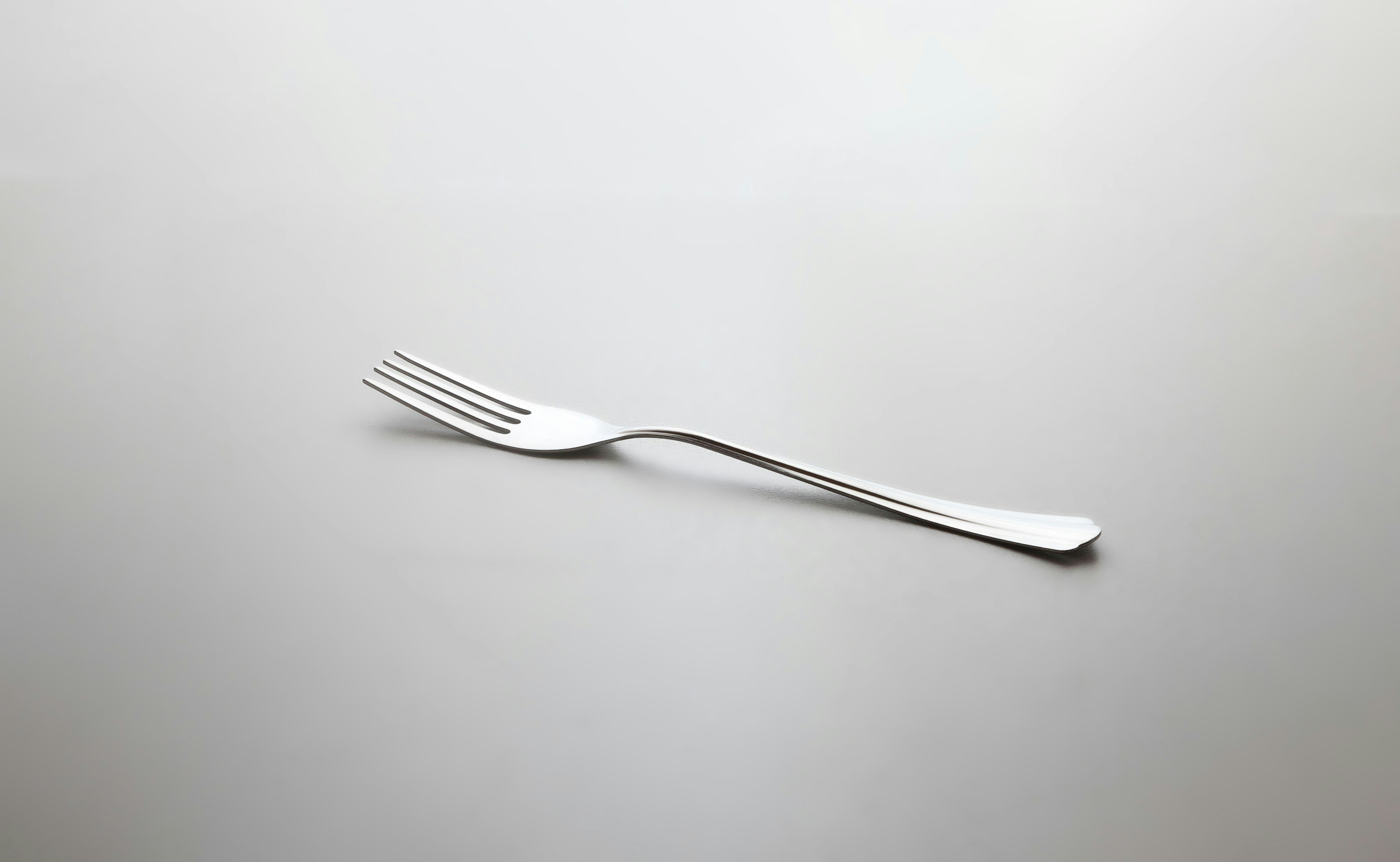 A sleek, silver fork elegantly positioned on a smooth, neutral background, emphasizing its design and form.