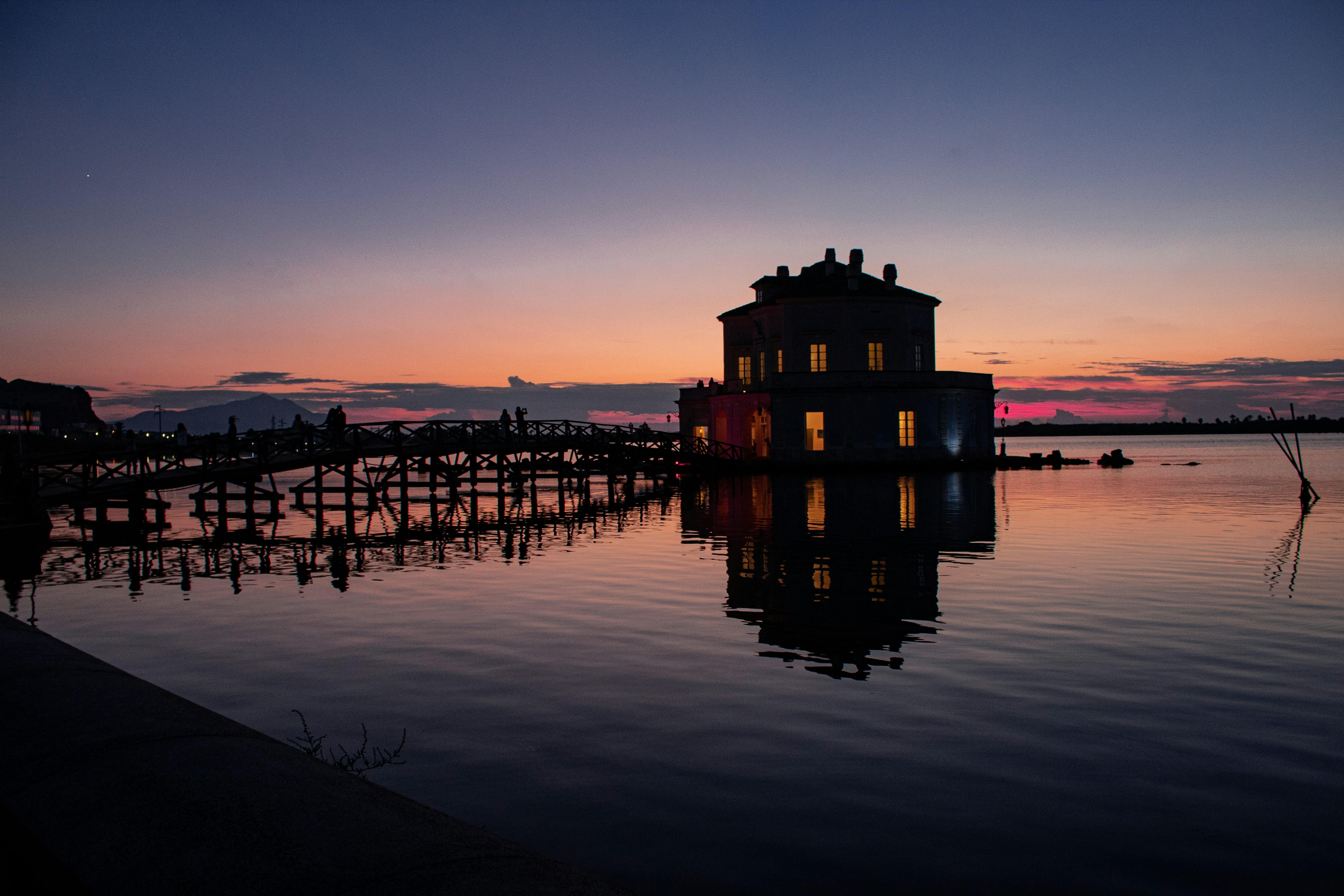 Silhouette of a lakeside building against a vibrant sunset with calm waters reflecting the sky.