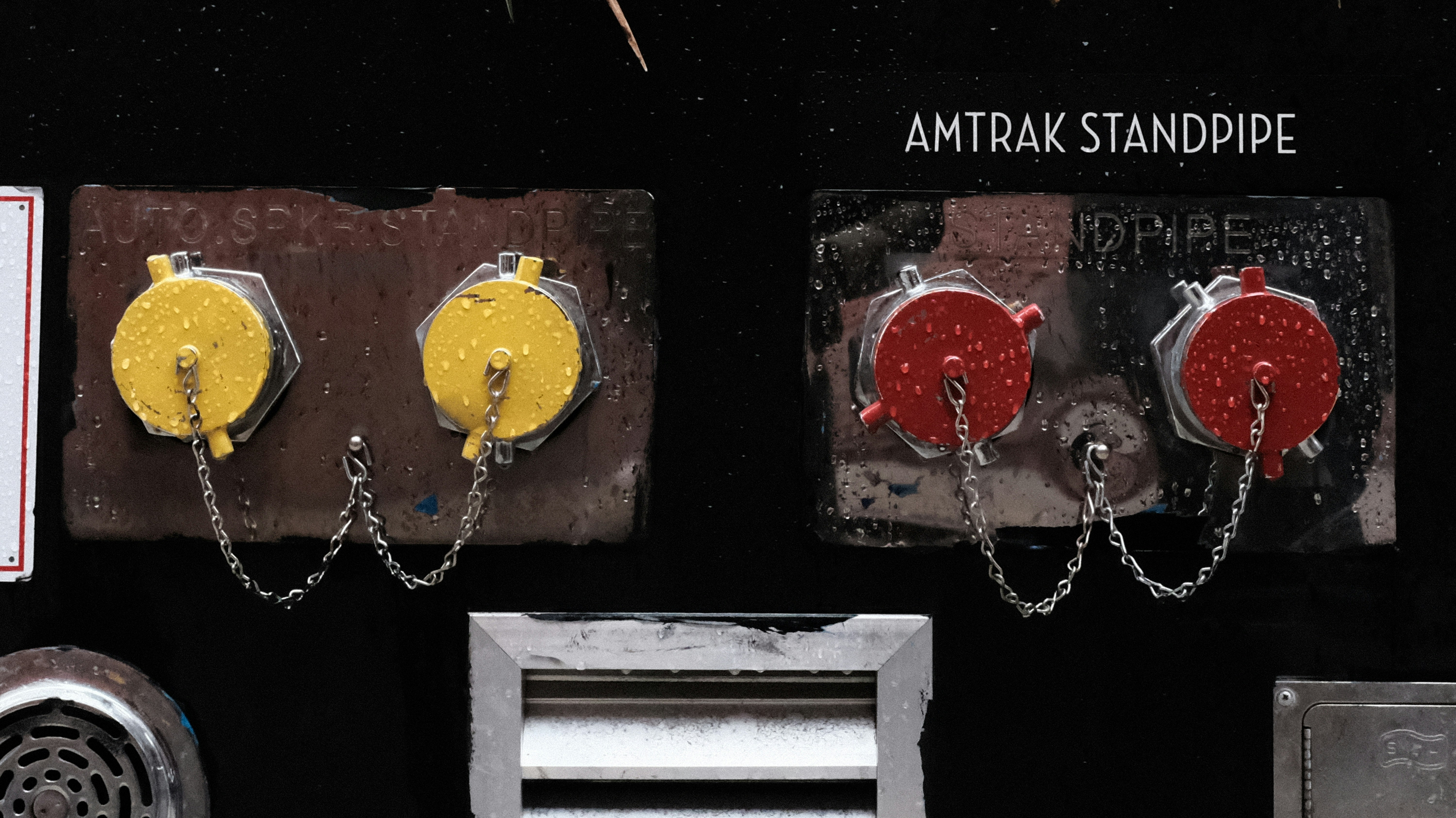 Colorful yellow and red standpipes with chains set against a dark industrial background.