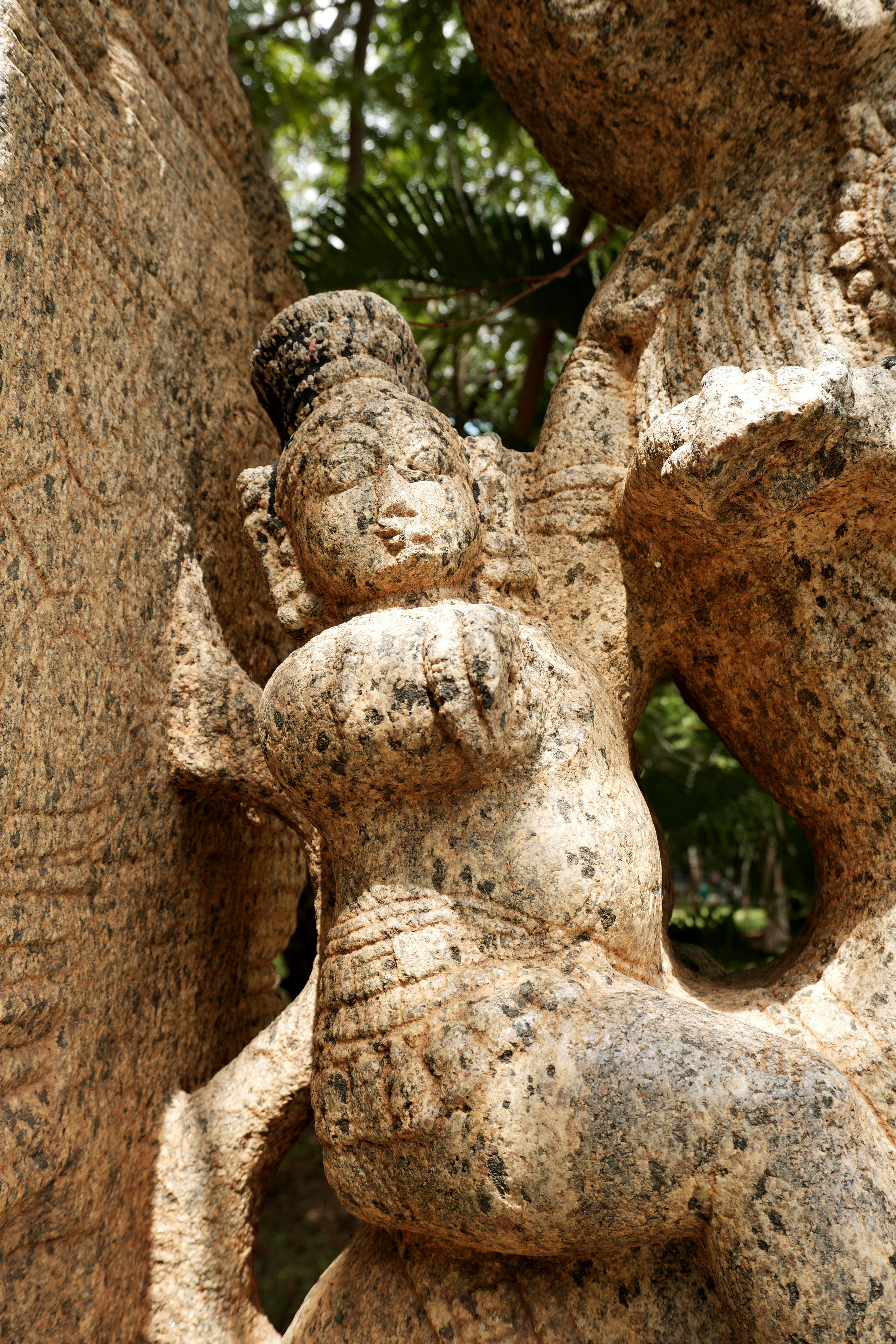 Intricately carved stone sculpture depicting a figure in a dynamic pose, surrounded by textured rock formations. The work highlights the artistry of ancient craftsmanship.