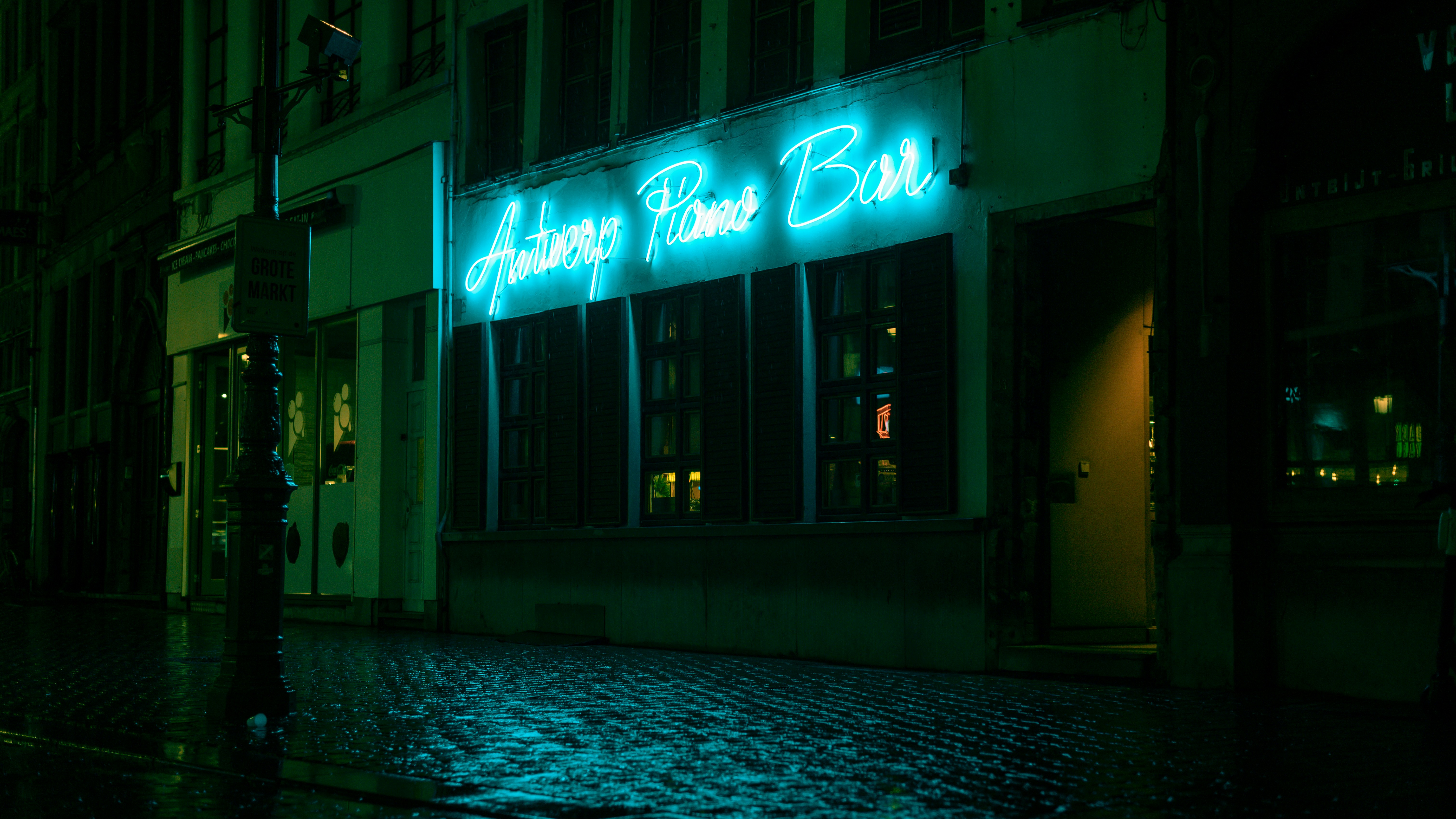 Neon sign glowing above wet cobblestones at night.