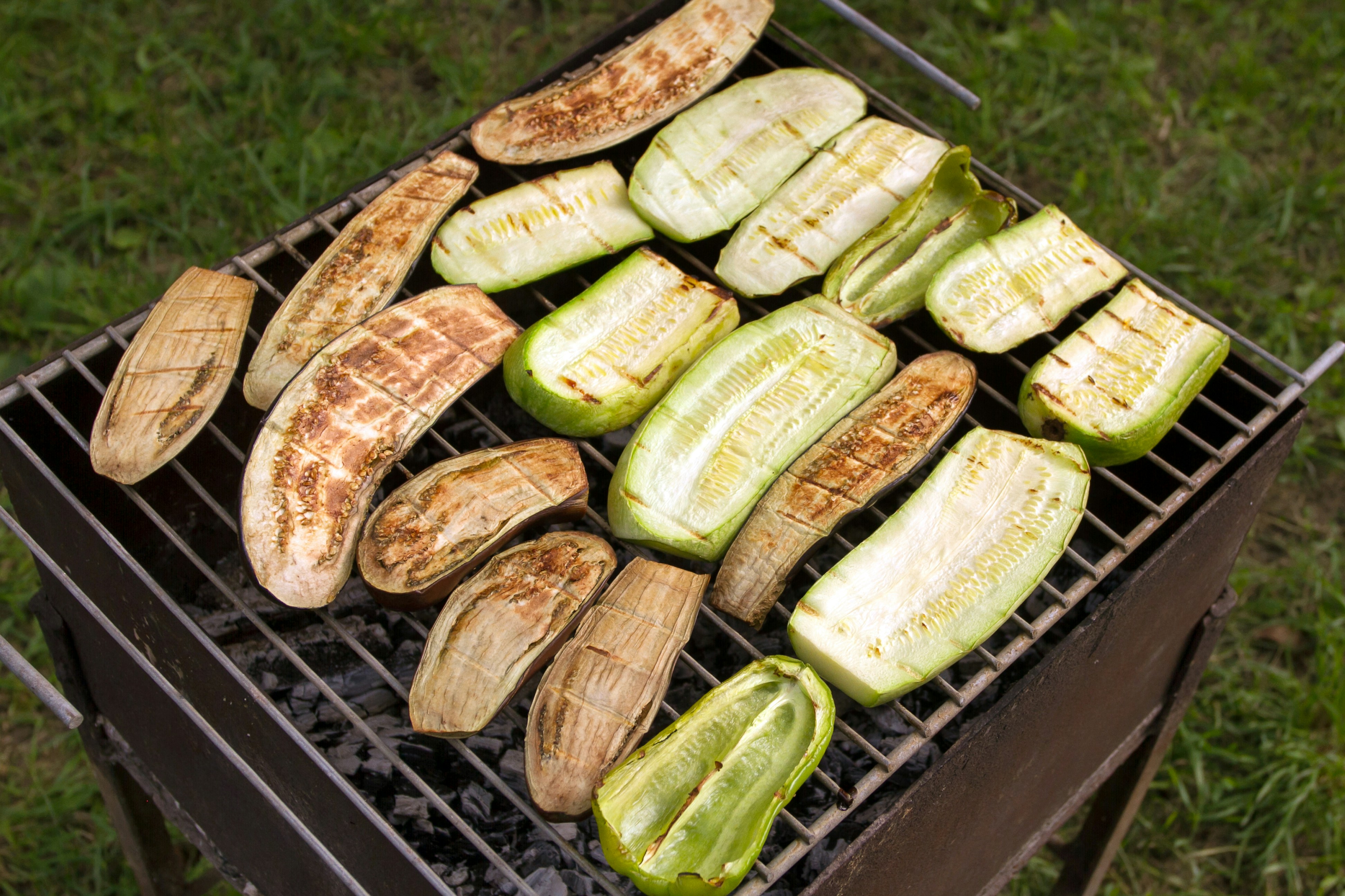 Sliced green bananas and plantains grilling on a charcoal barbecue, showcasing their charred textures and vibrant colors.