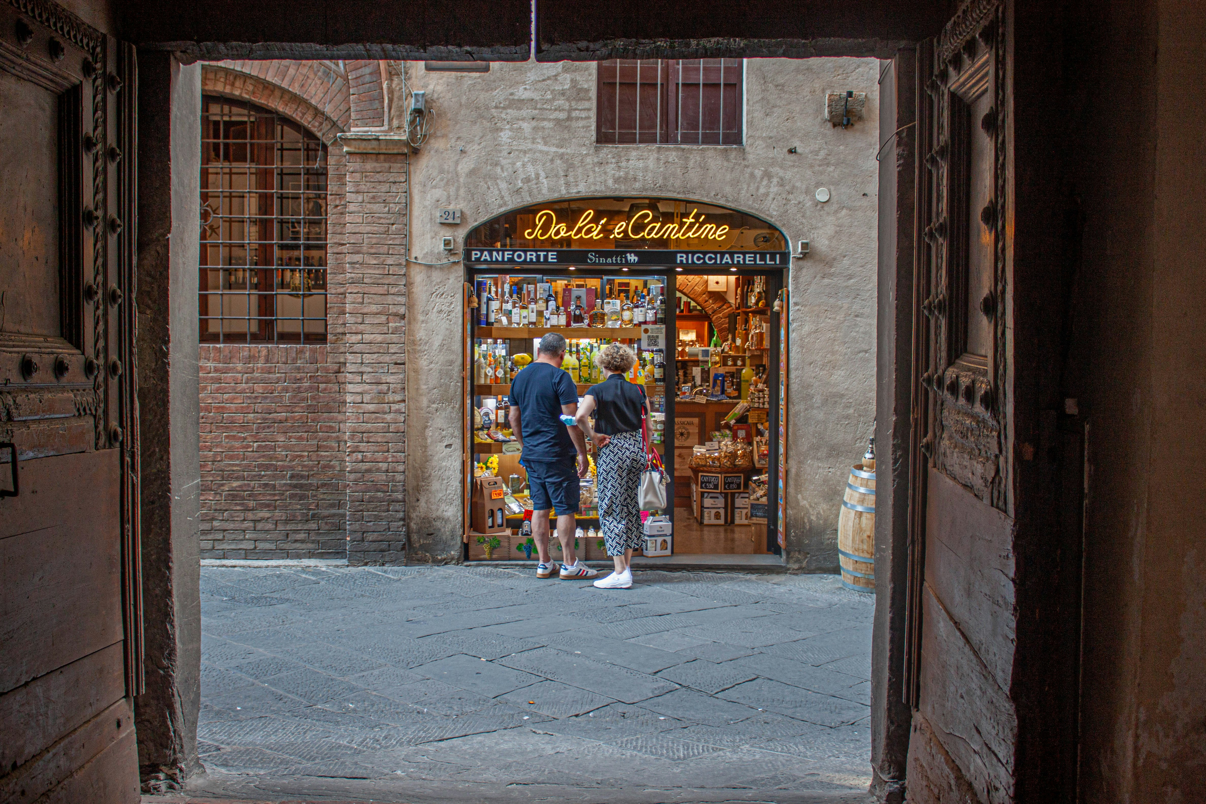 Couple exploring a charming shop filled with local delicacies and artisanal products, framed by an ancient doorway.