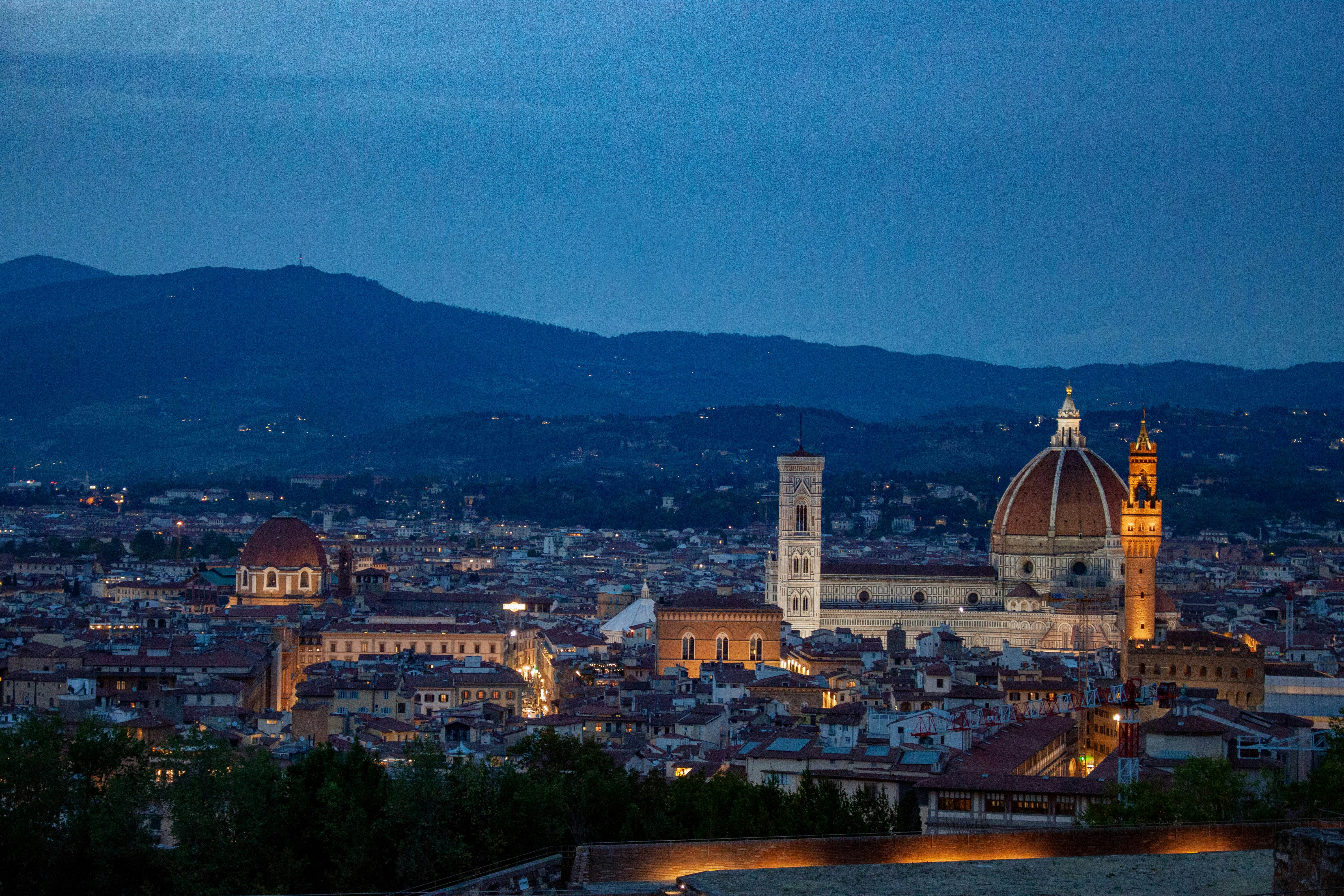 Florence cityscape at dusk with illuminated cathedral and distant mountains.