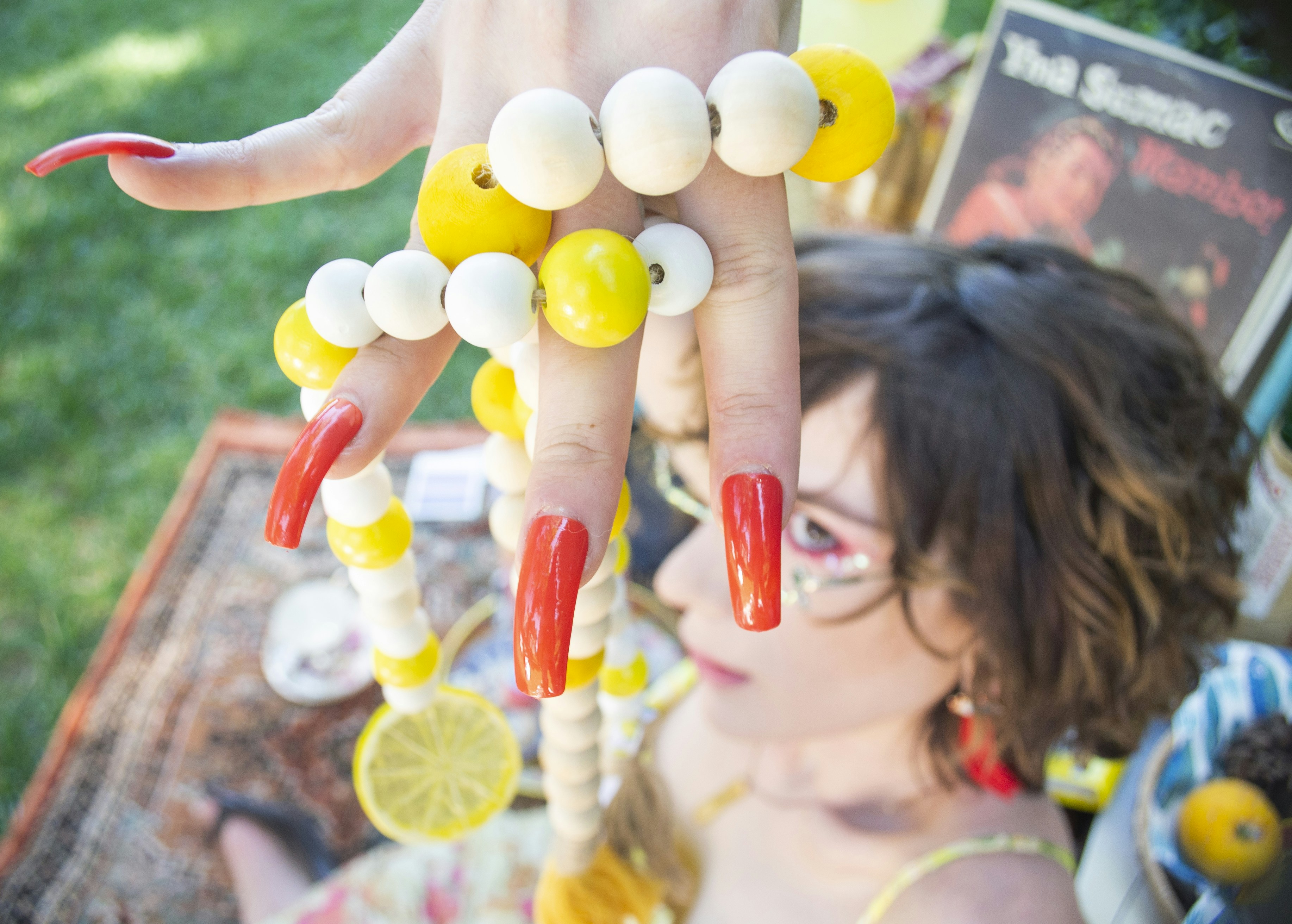 Lemon-Bead Cascade: A Sunlit Hand Portrait with Red Nails