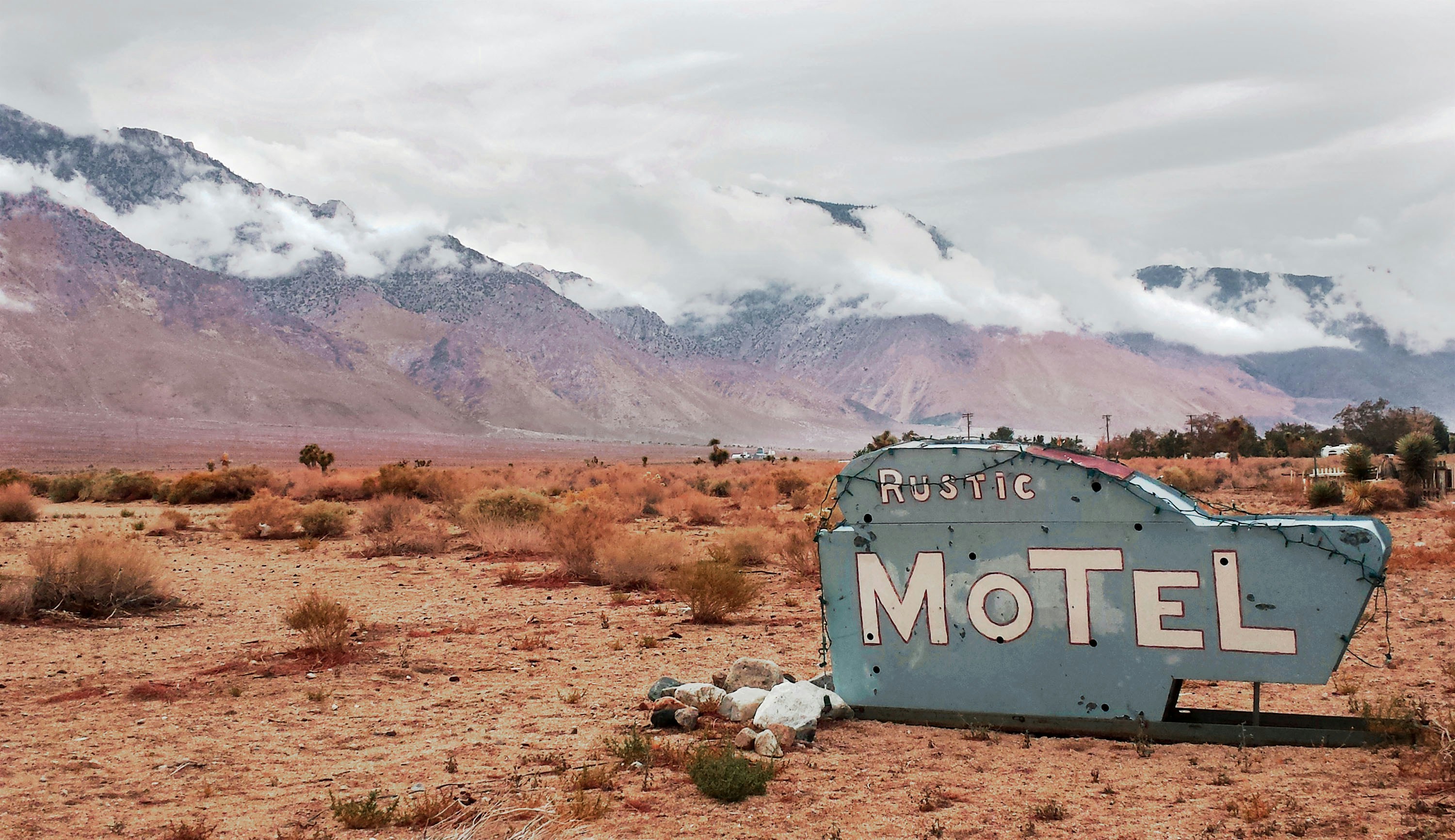 Weathered sign of a rustic motel stands against a backdrop of mountains shrouded in clouds, evoking a sense of nostalgia and solitude.