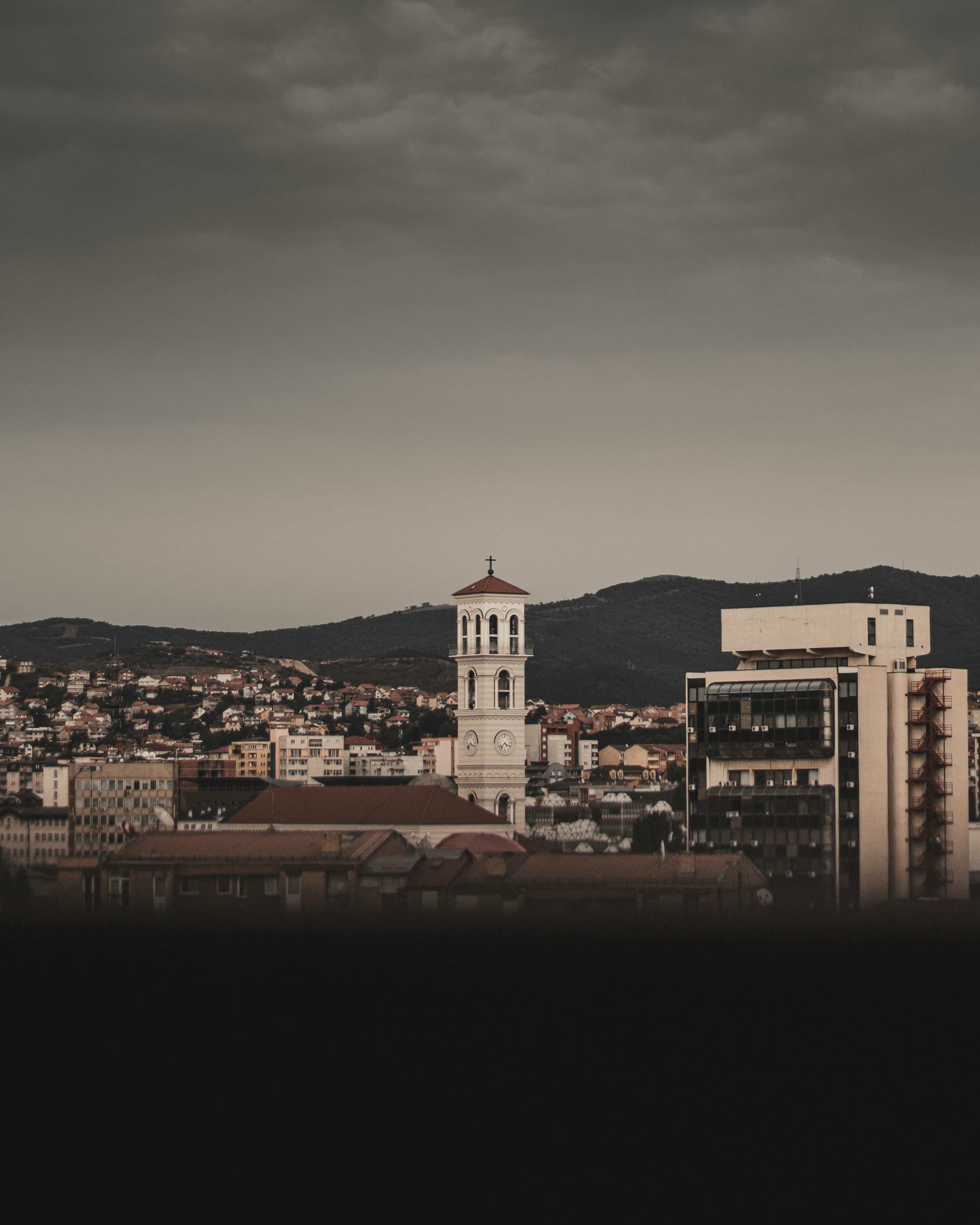 Cityscape with a prominent cathedral tower and surrounding modern buildings under a cloudy sky.