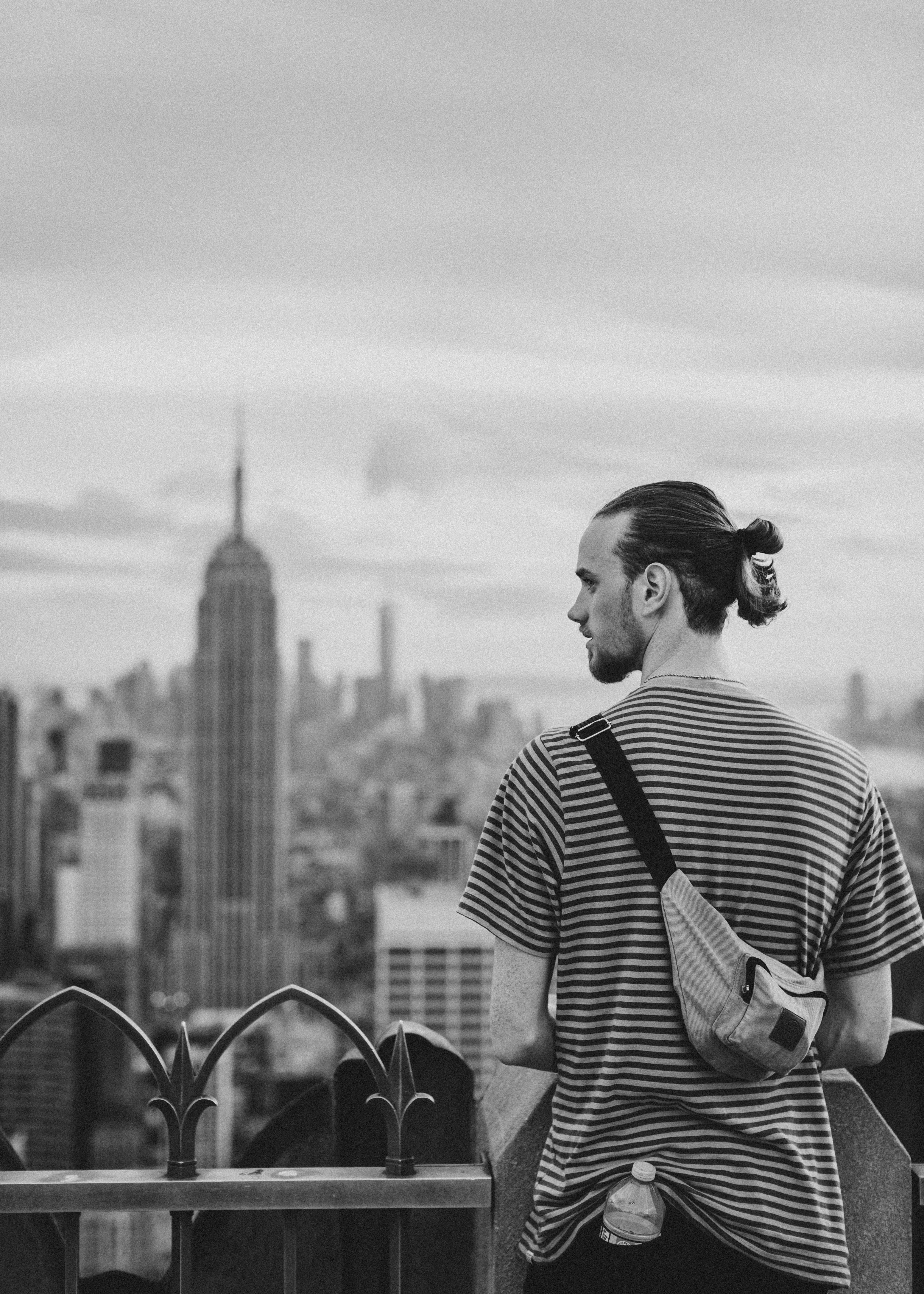 Rooftop Gaze: A striped-shirt wanderer surveys a grayscale skyline.