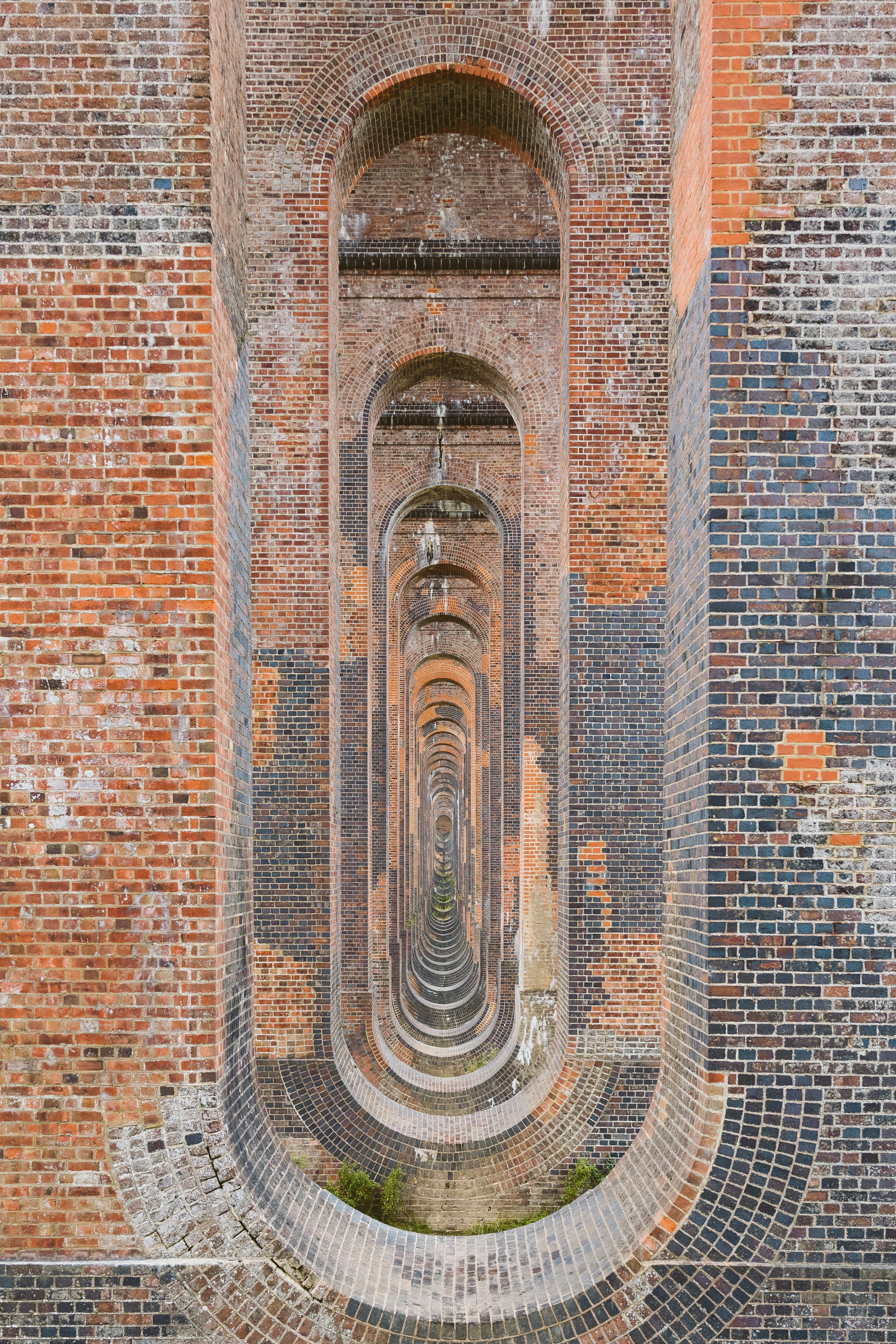 Intricate brick arches create a mesmerizing tunnel effect, showcasing the beauty of historical engineering. The perspective draws the eye toward a distant green landscape.