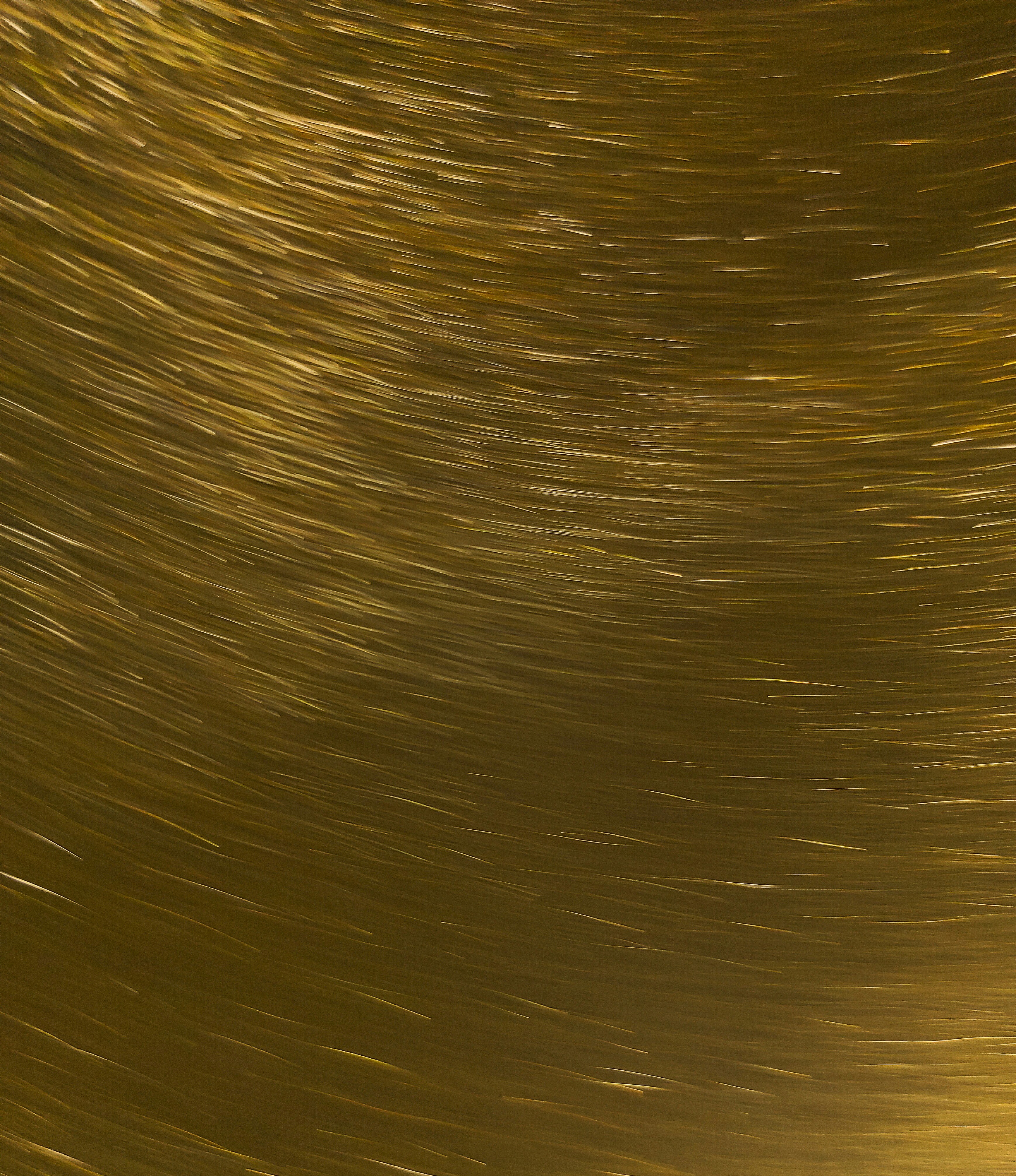 A close-up of vibrant, golden light trails forming circular streaks across a smooth surface. The abstract composition emphasizes texture and motion in warm tones.