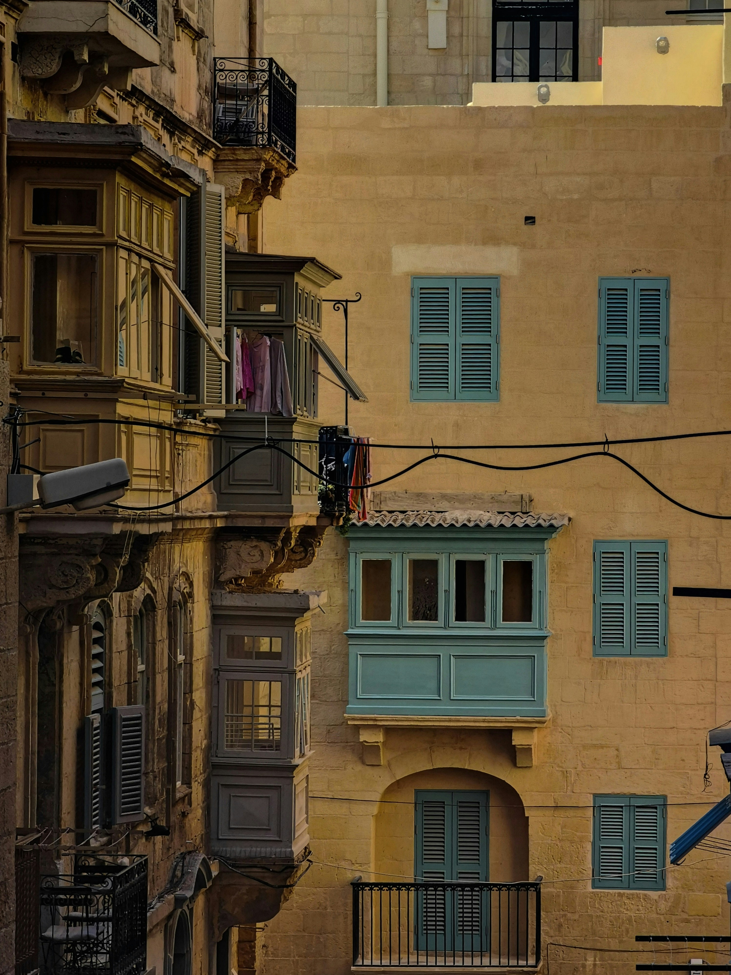 Blue Shuttered Veranda Framing a Sunlit Maltese Facade