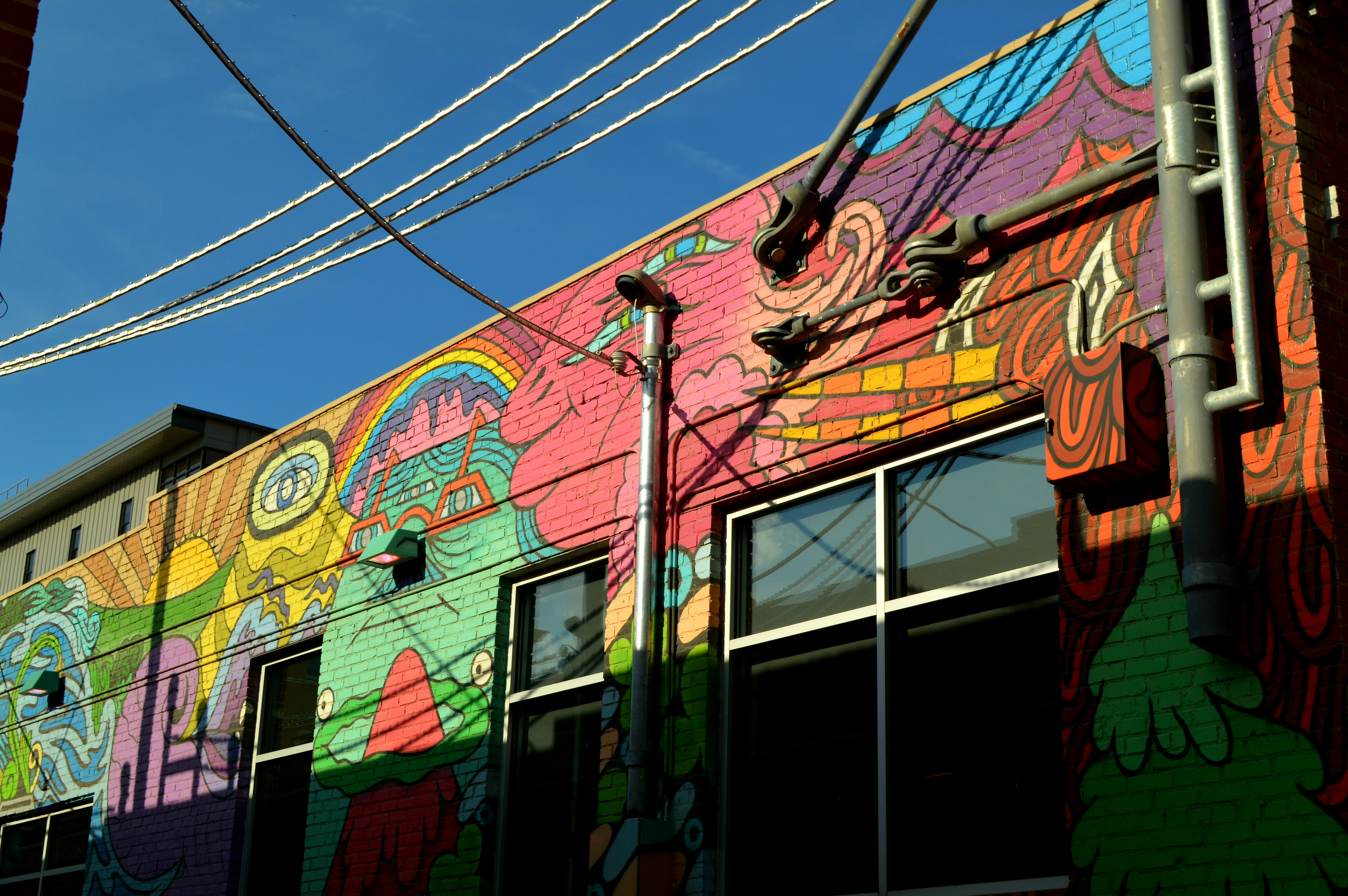 Colorful mural depicting whimsical landscapes on a building's side under a clear blue sky.