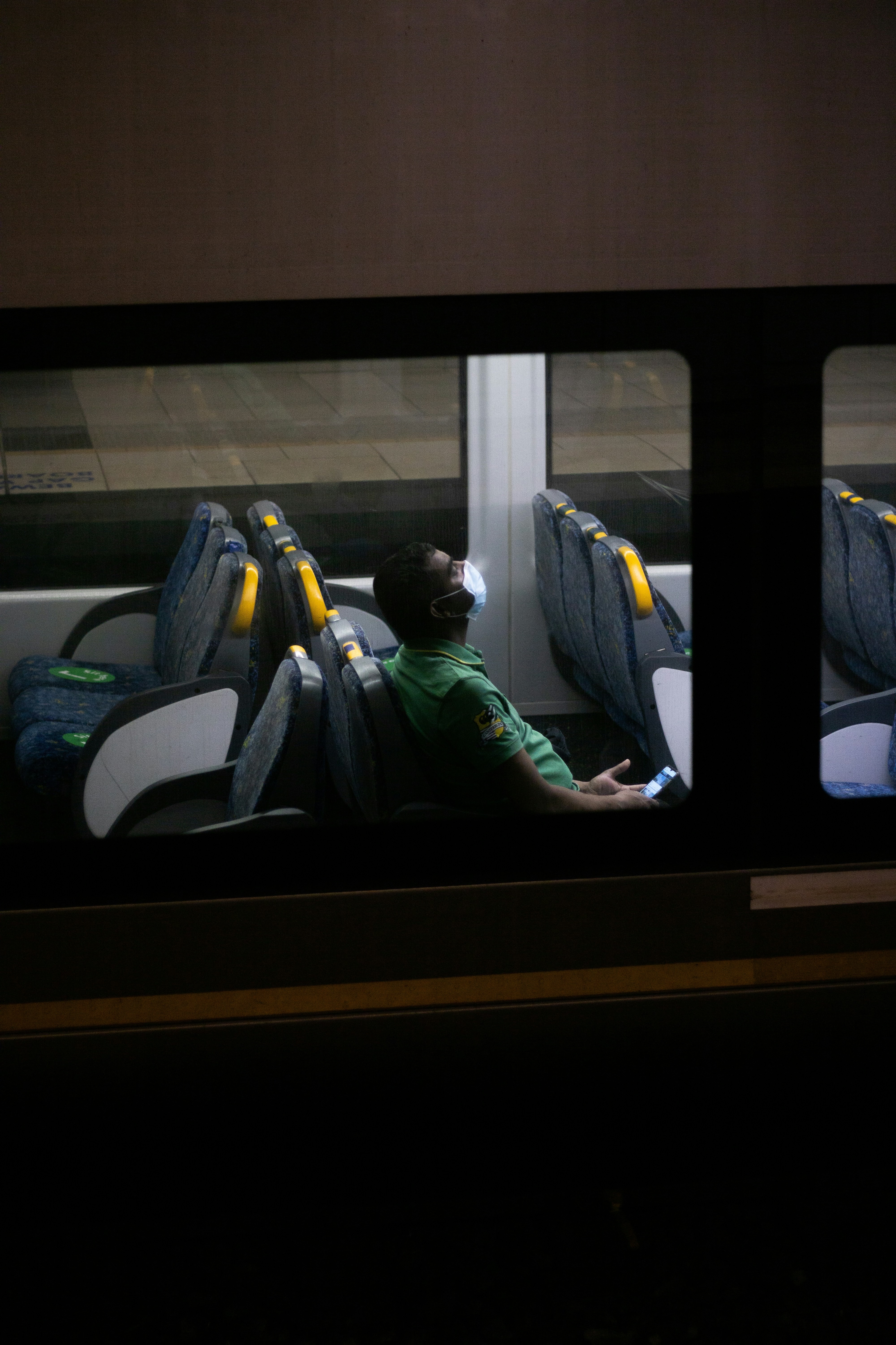 Masked traveler in a quiet train car, green shirt catching a moment of stillness