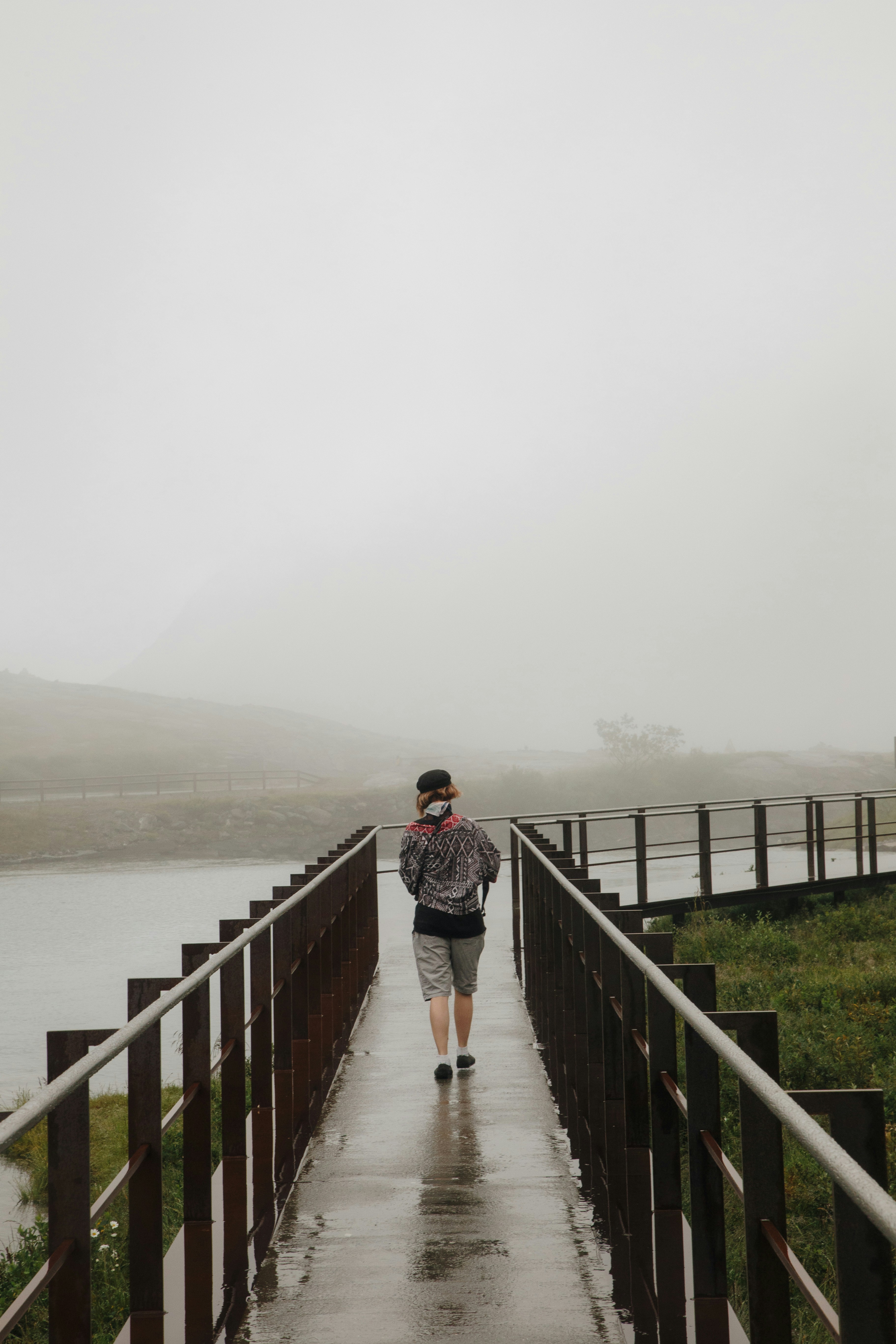 Fogbound Footbridge: A lone traveler on a rain-washed boardwalk