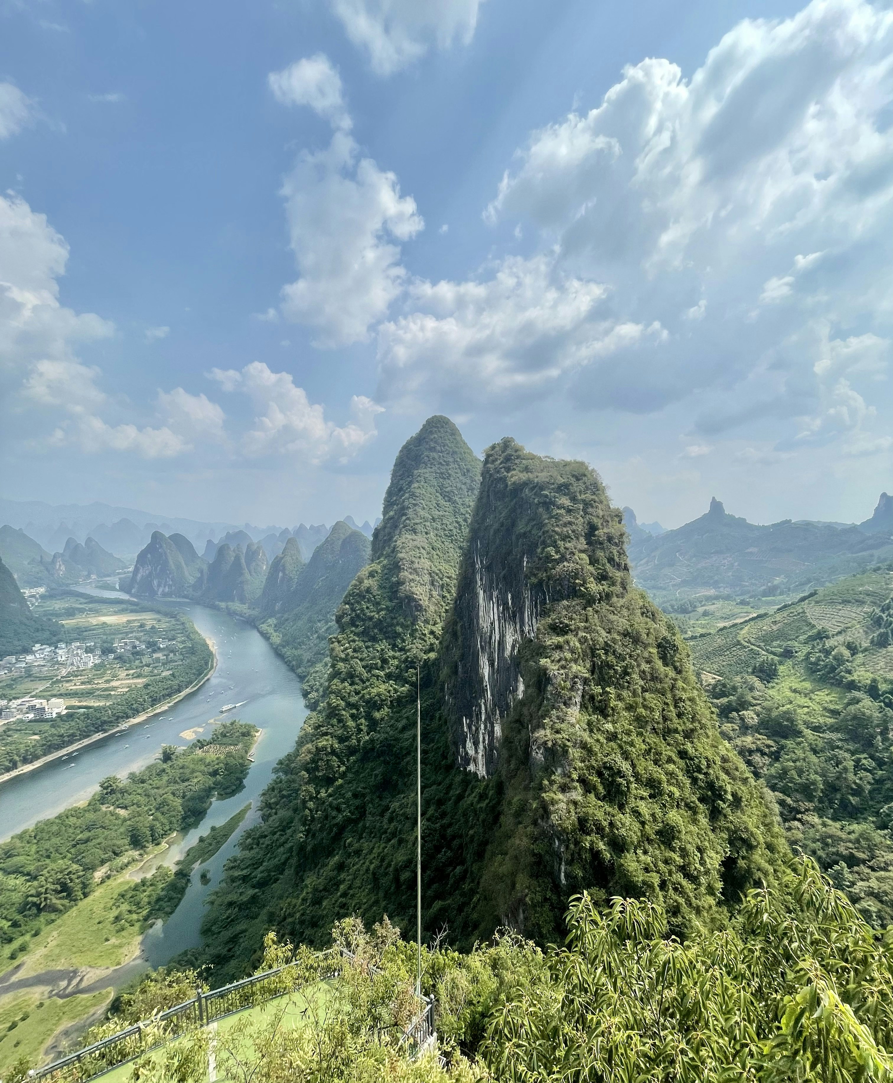 Aerial photograph of towering karst spires and a winding river through a green valley, with a dominant central spike.