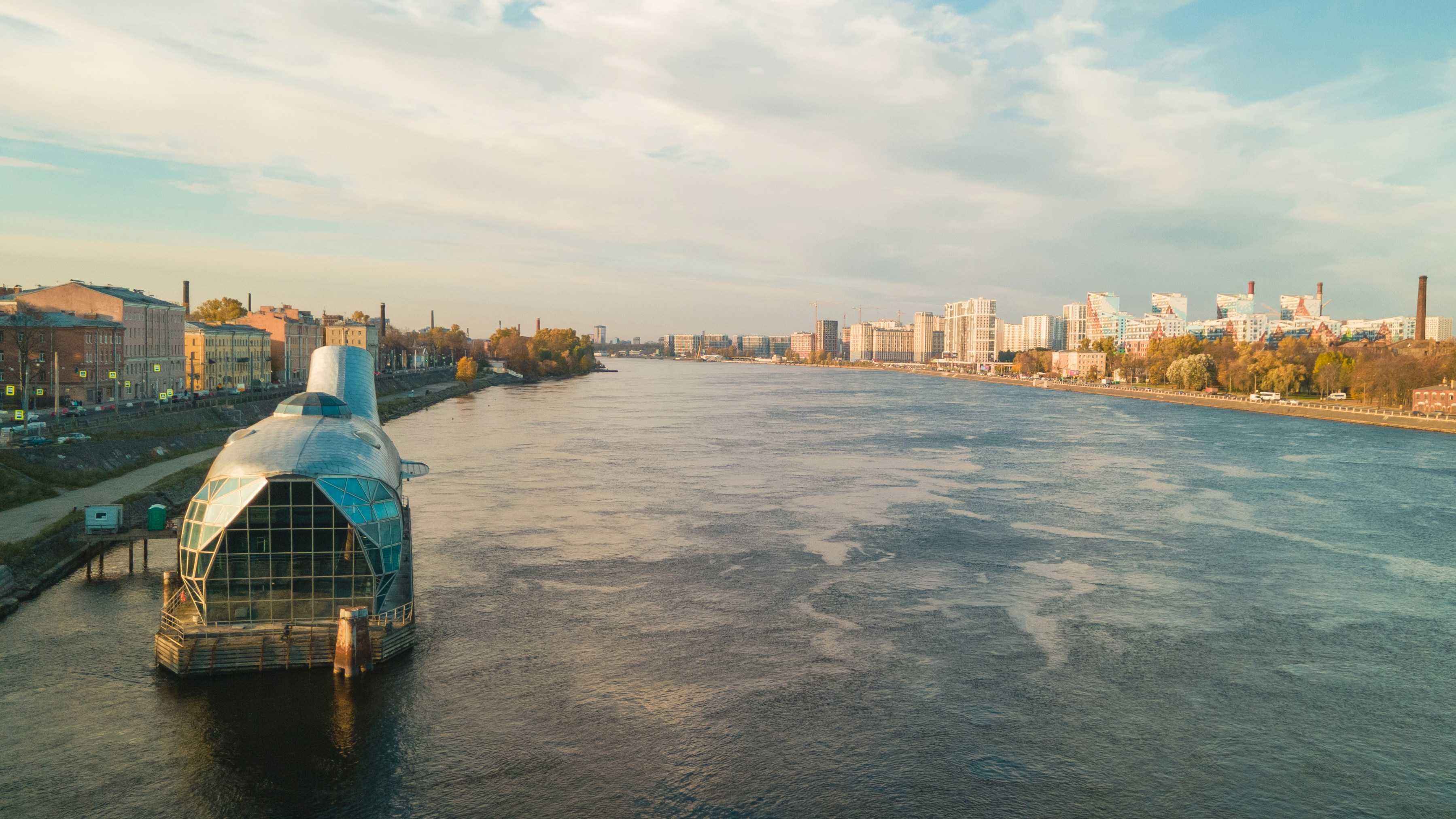 Modern glass structure by the riverbank reflects the urban landscape, showcasing a blend of nature and architecture.