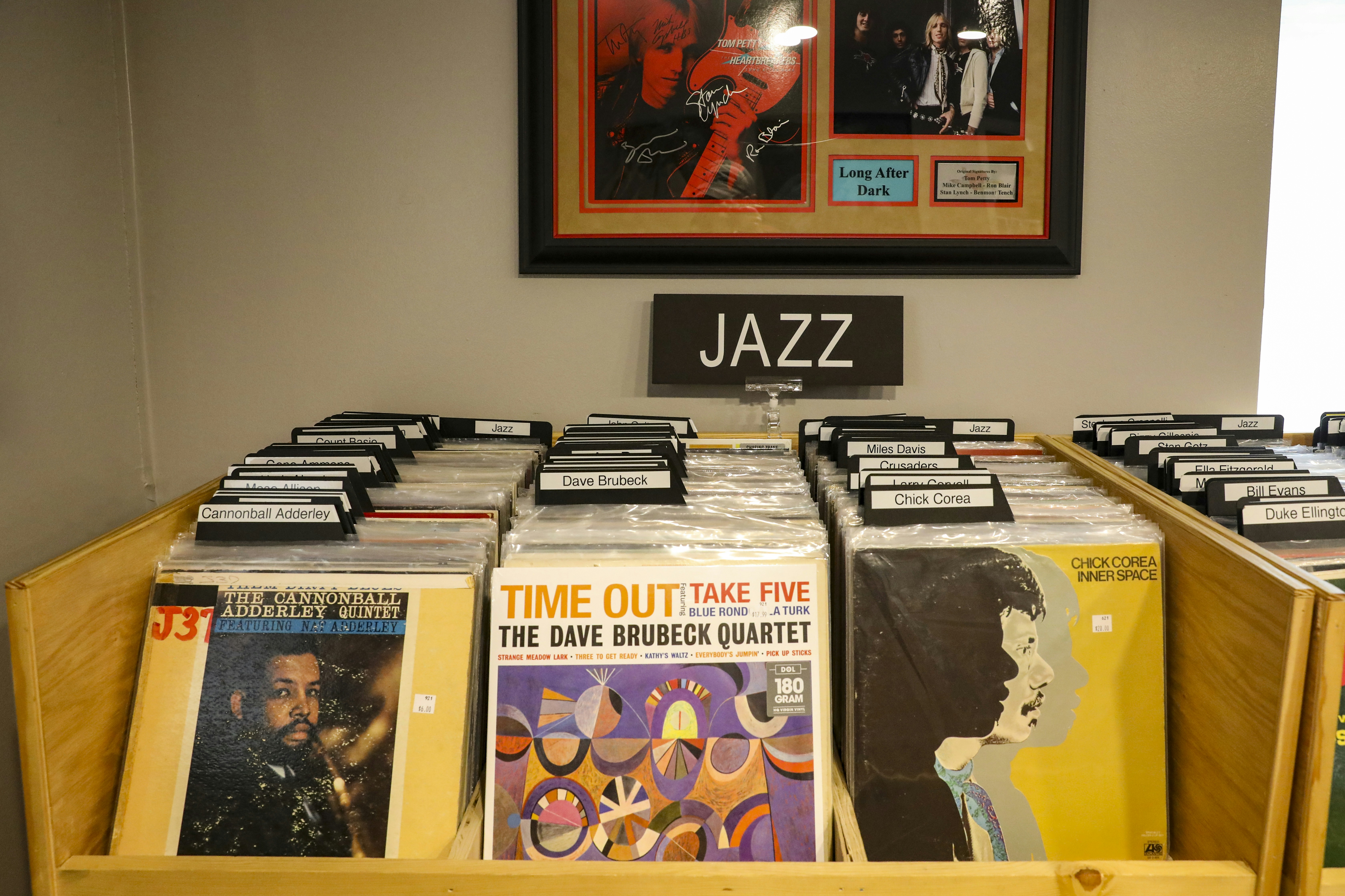 Wooden rack filled with jazz vinyl records beneath a framed poster in a record store.