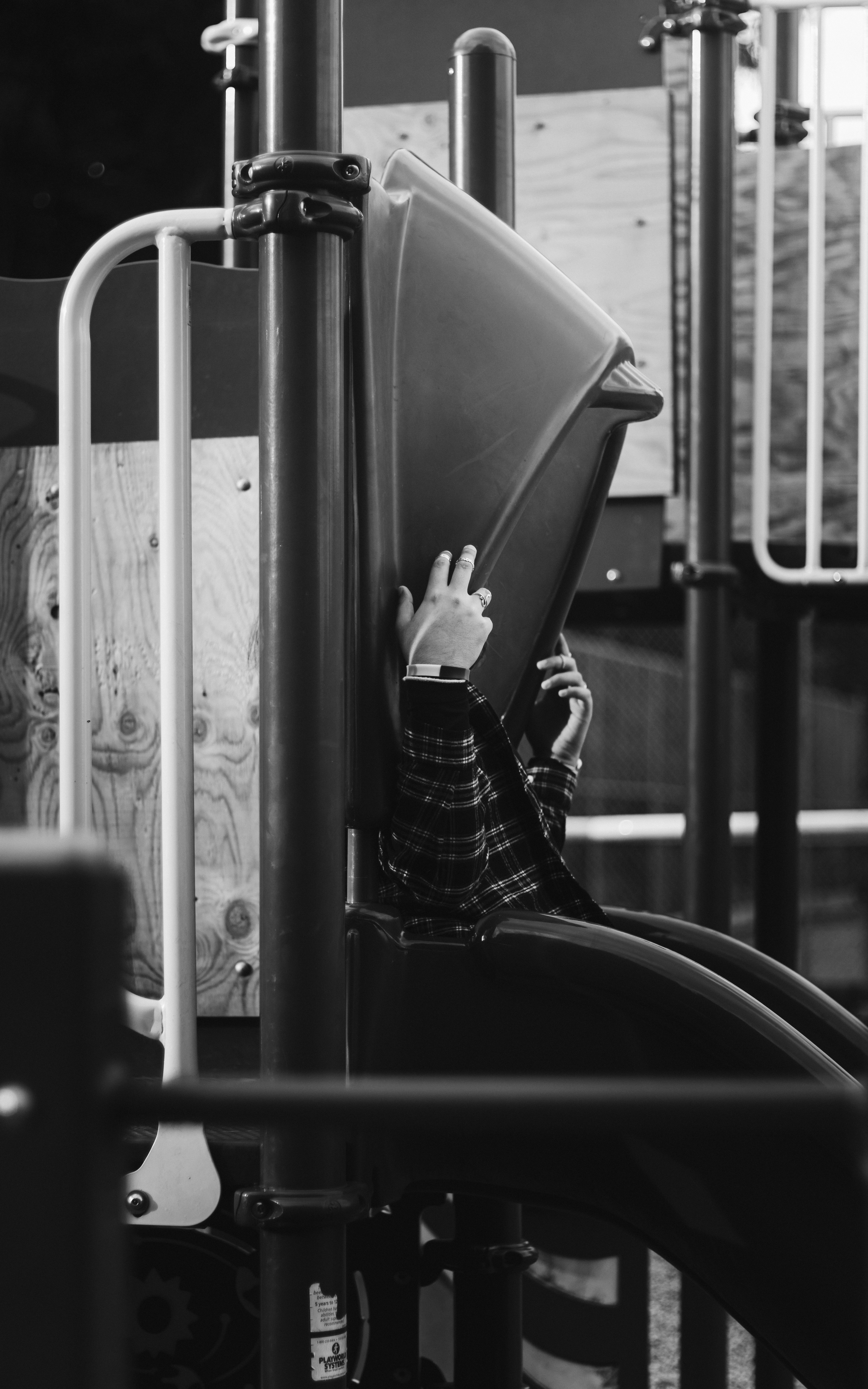 A child playfully peeks from behind a slide's cover, embodying the spirit of childhood exploration. The scene captures the essence of play in a monochrome setting.