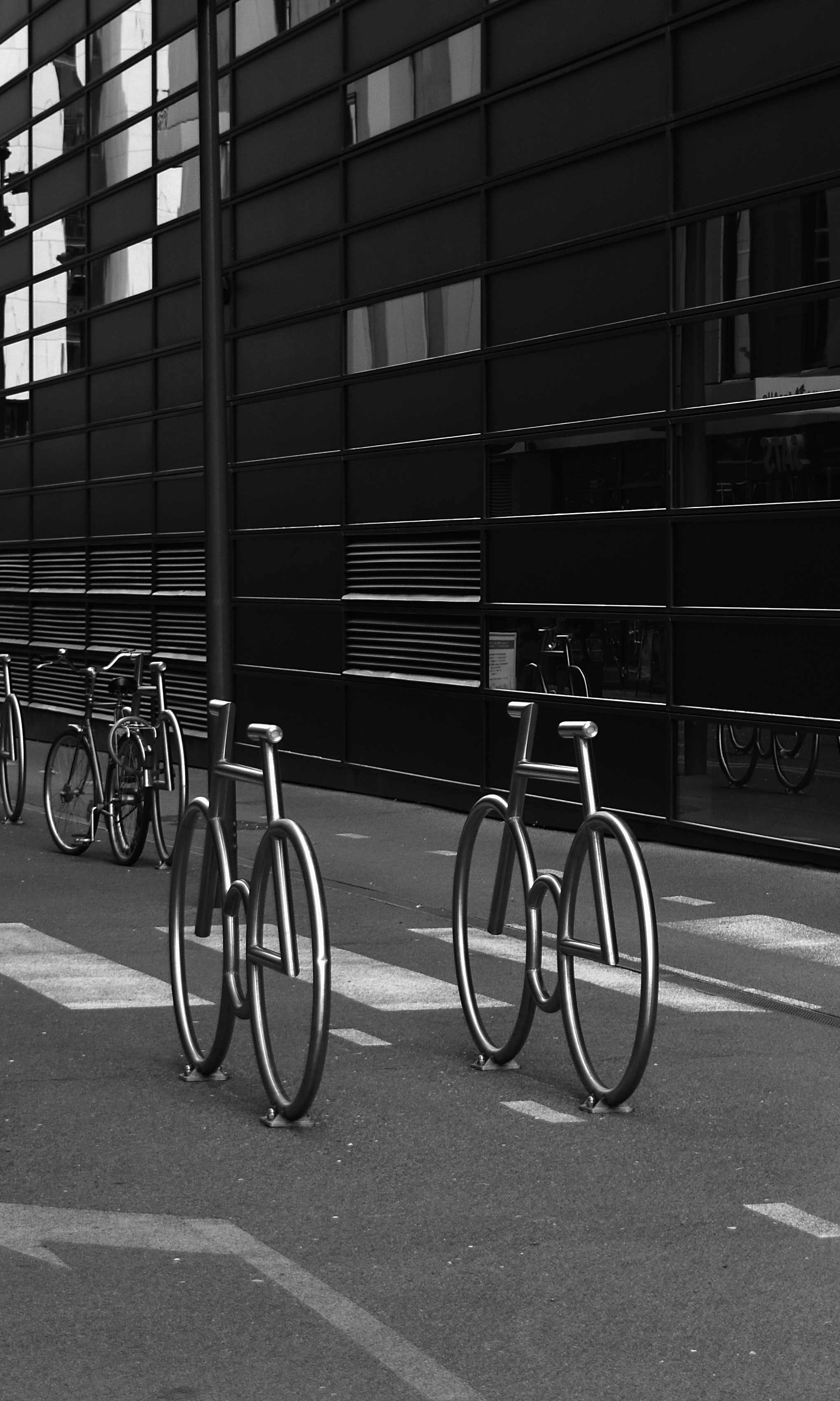 Stylized bicycle racks resembling bicycles, set against a sleek, reflective building facade. The monochrome palette enhances the contemporary urban aesthetic.