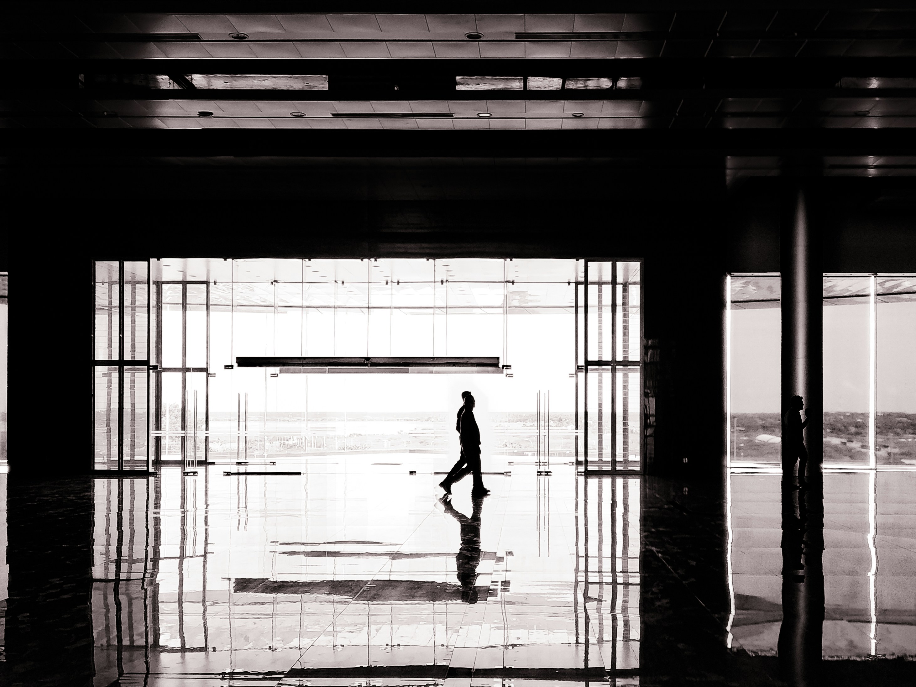 Silhouette of a person walking through a sunlit atrium with reflective flooring.