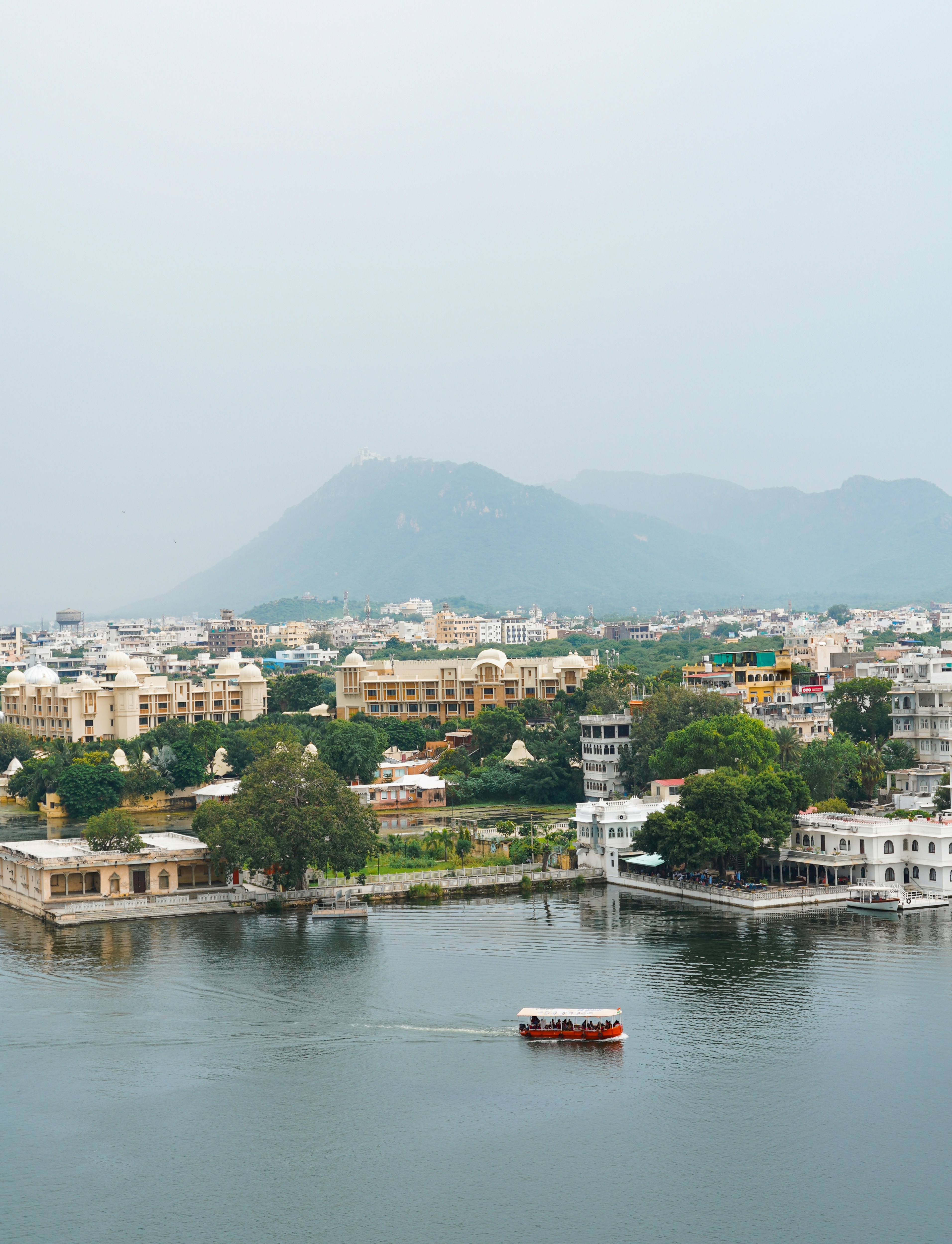 A serene view of a lakeside city with lush greenery and traditional architecture, complemented by a small boat gliding across the water.