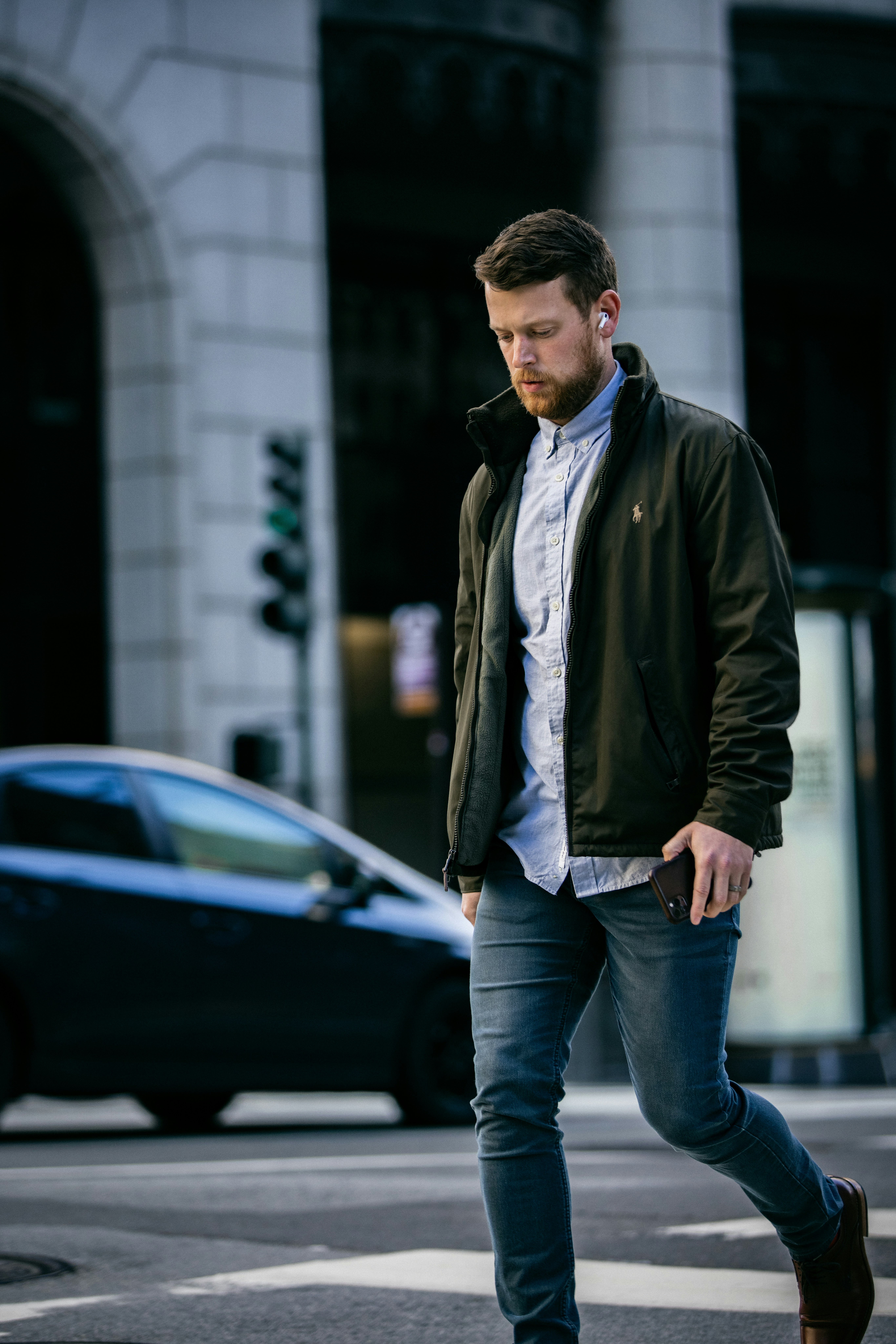 Man walking on city street, absorbed in thought with earbuds in, as traffic flows by in the background.