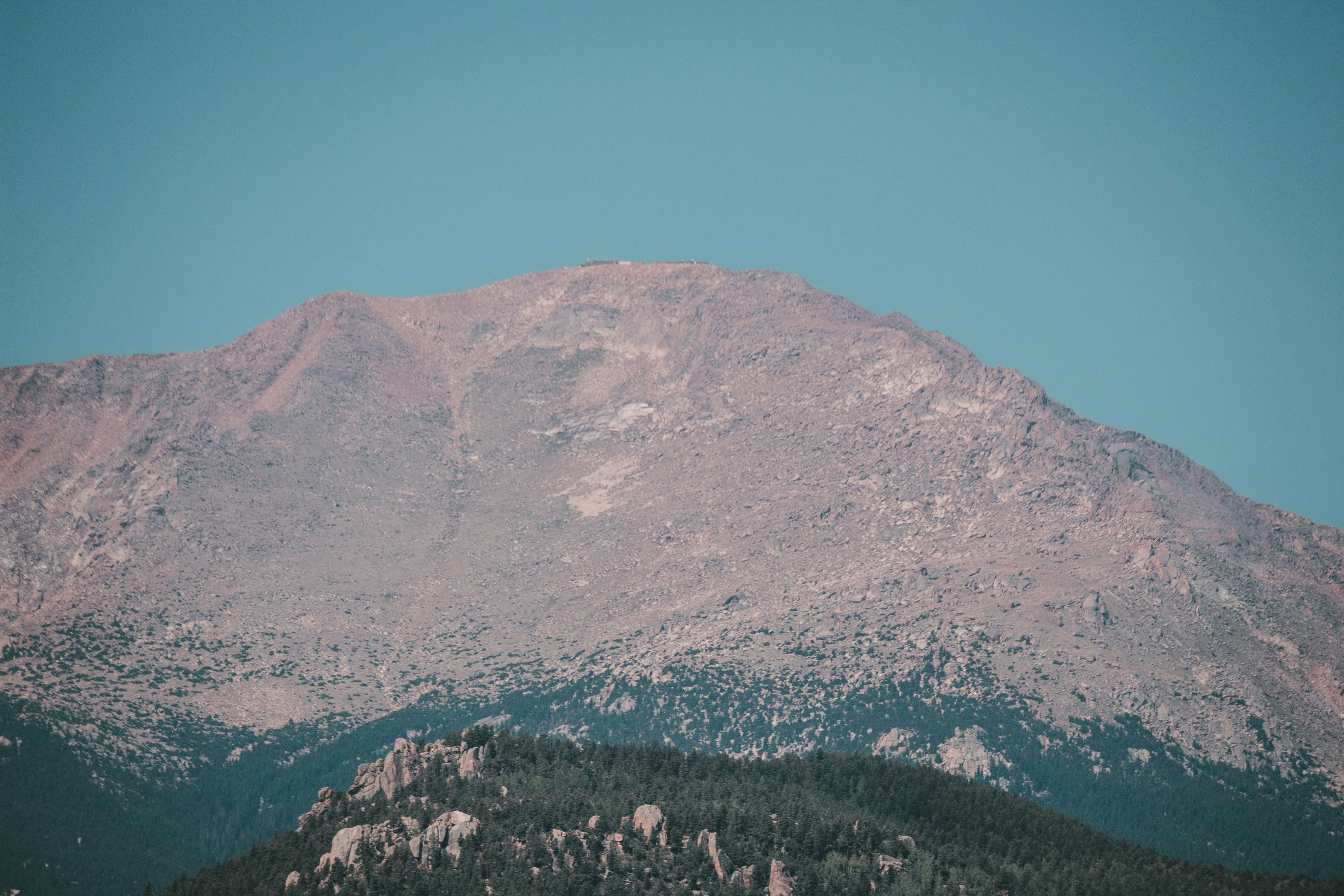 Majestic mountain peak towering over a lush forest, bathed in soft, pastel hues under a clear sky.
