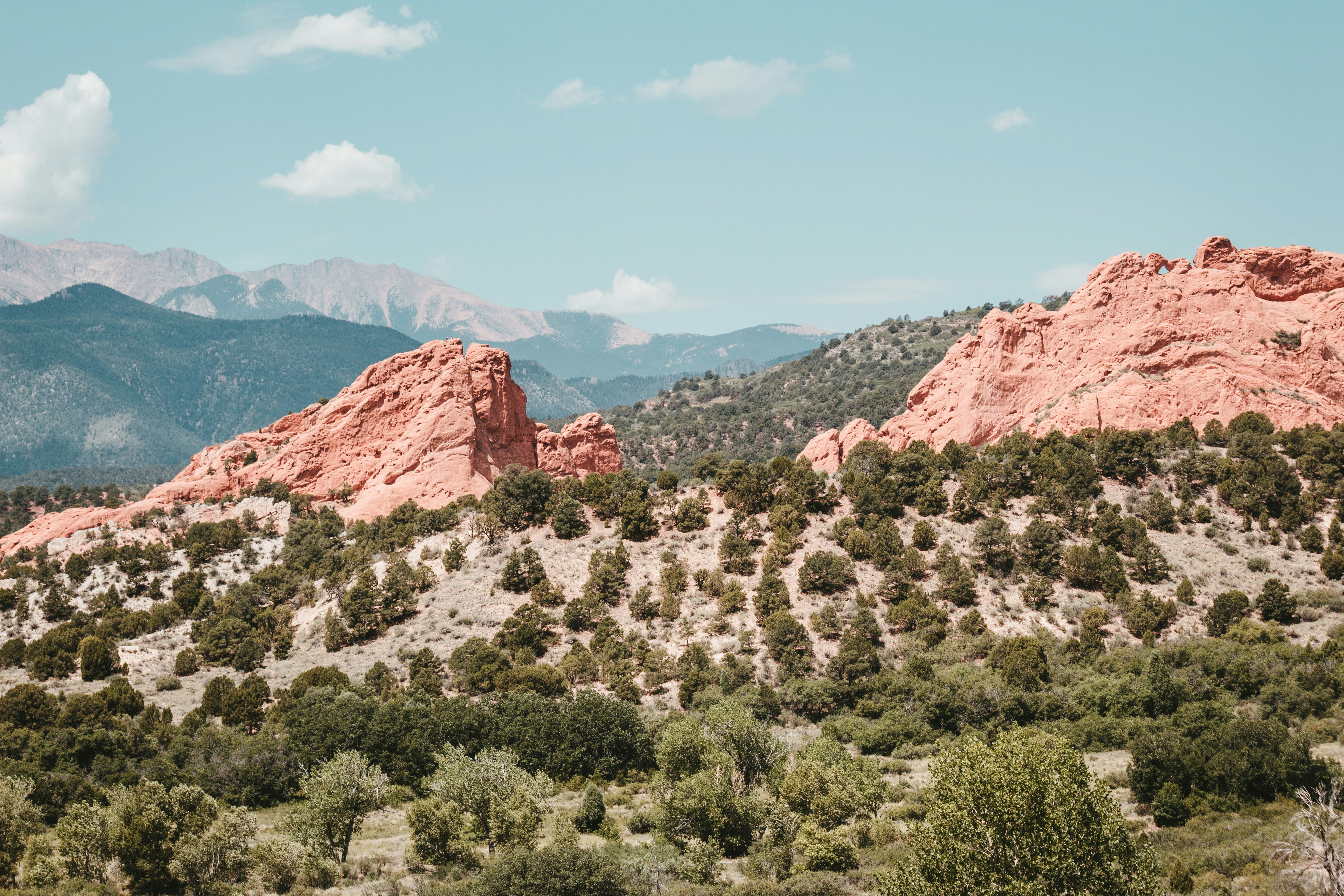 Vibrant red rock formations rise above a verdant landscape, showcasing the contrast between natural elements under a clear blue sky.