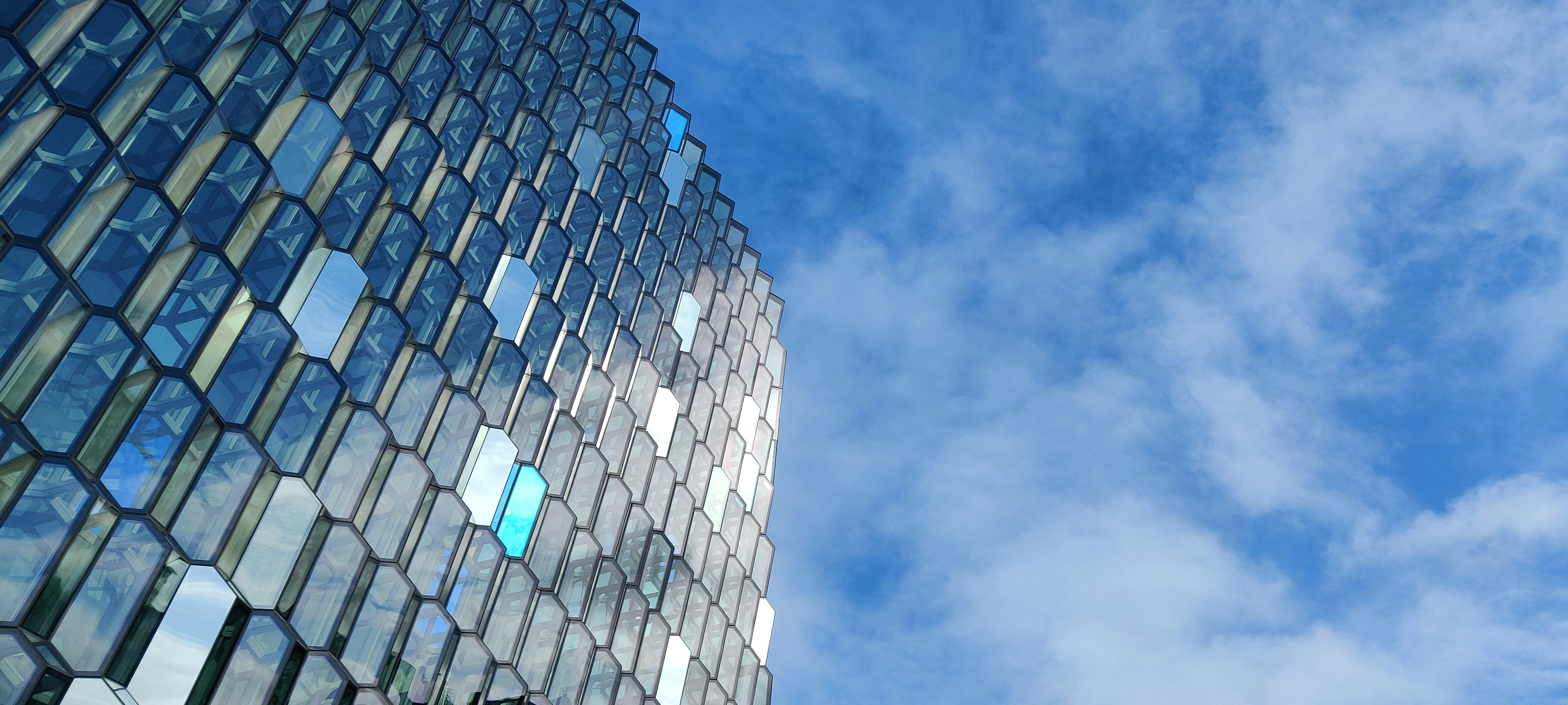 Abstract architectural design featuring a glass facade reflecting the sky and clouds. The interplay of light and structure highlights contemporary urban aesthetics.