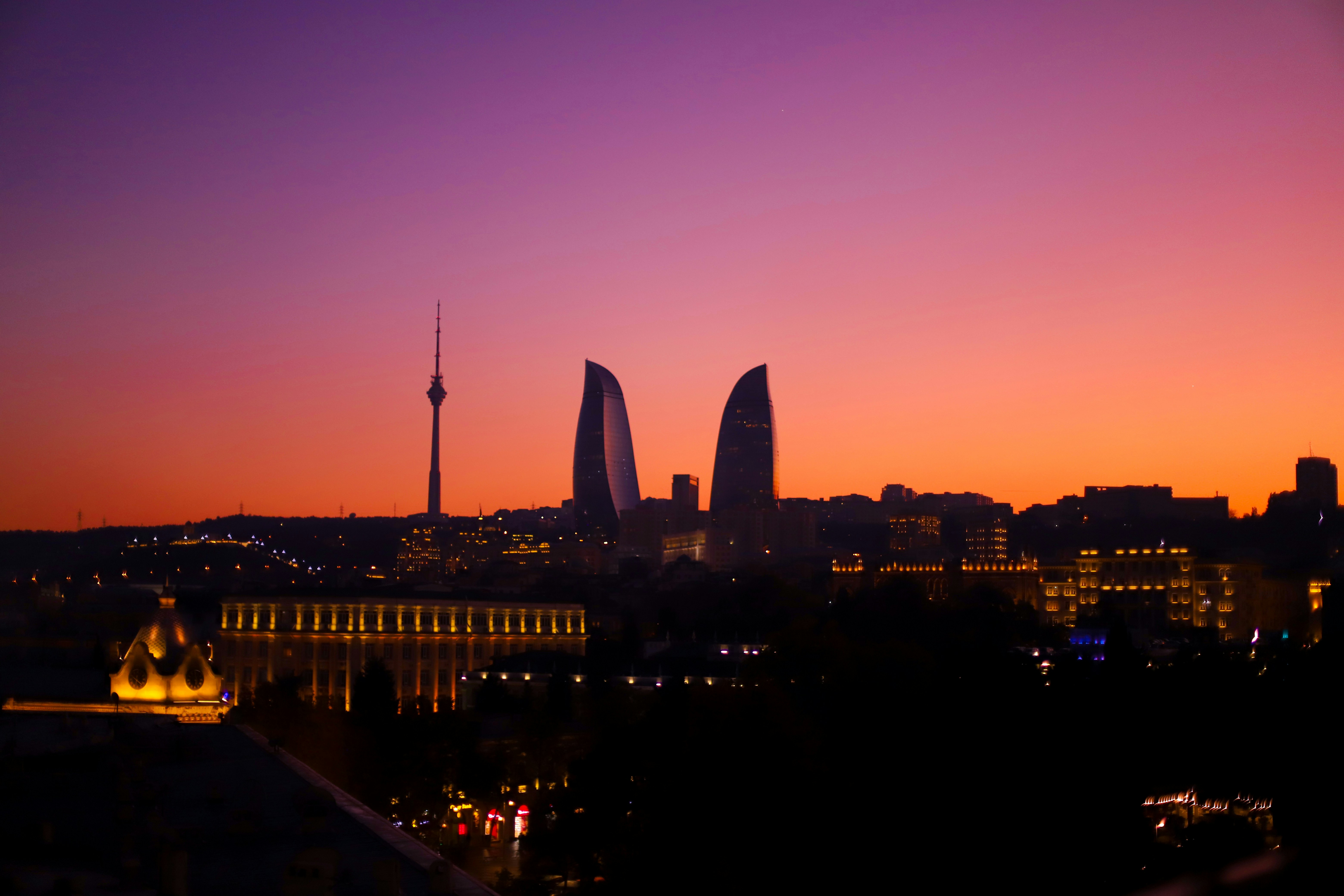 Silhouetted skyline of Baku at twilight, featuring the Flame Towers and a communications tower against a vibrant gradient sky.