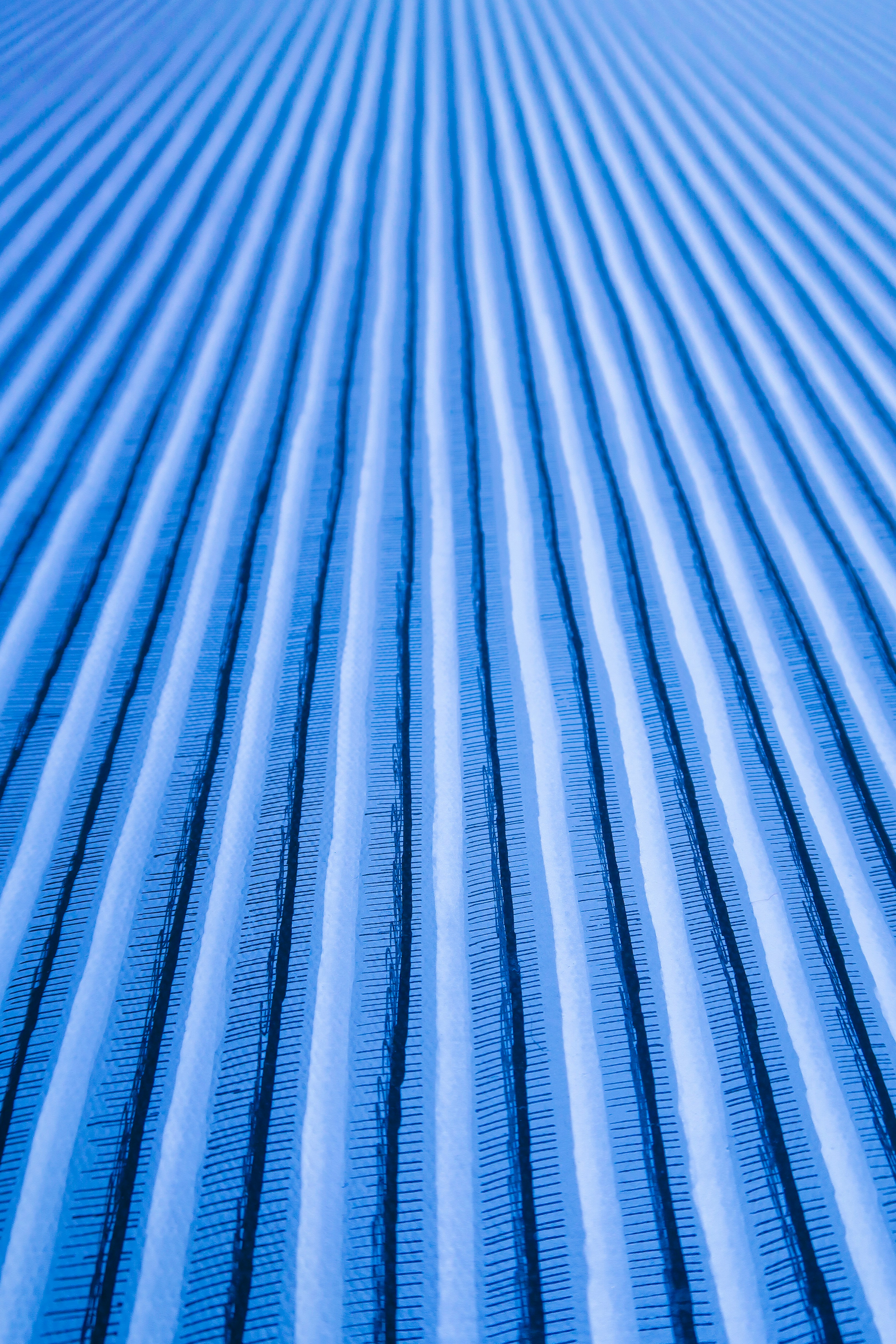 Abstract pattern of blue lines creating a rhythmic texture on a surface. The interplay of light enhances the visual depth.