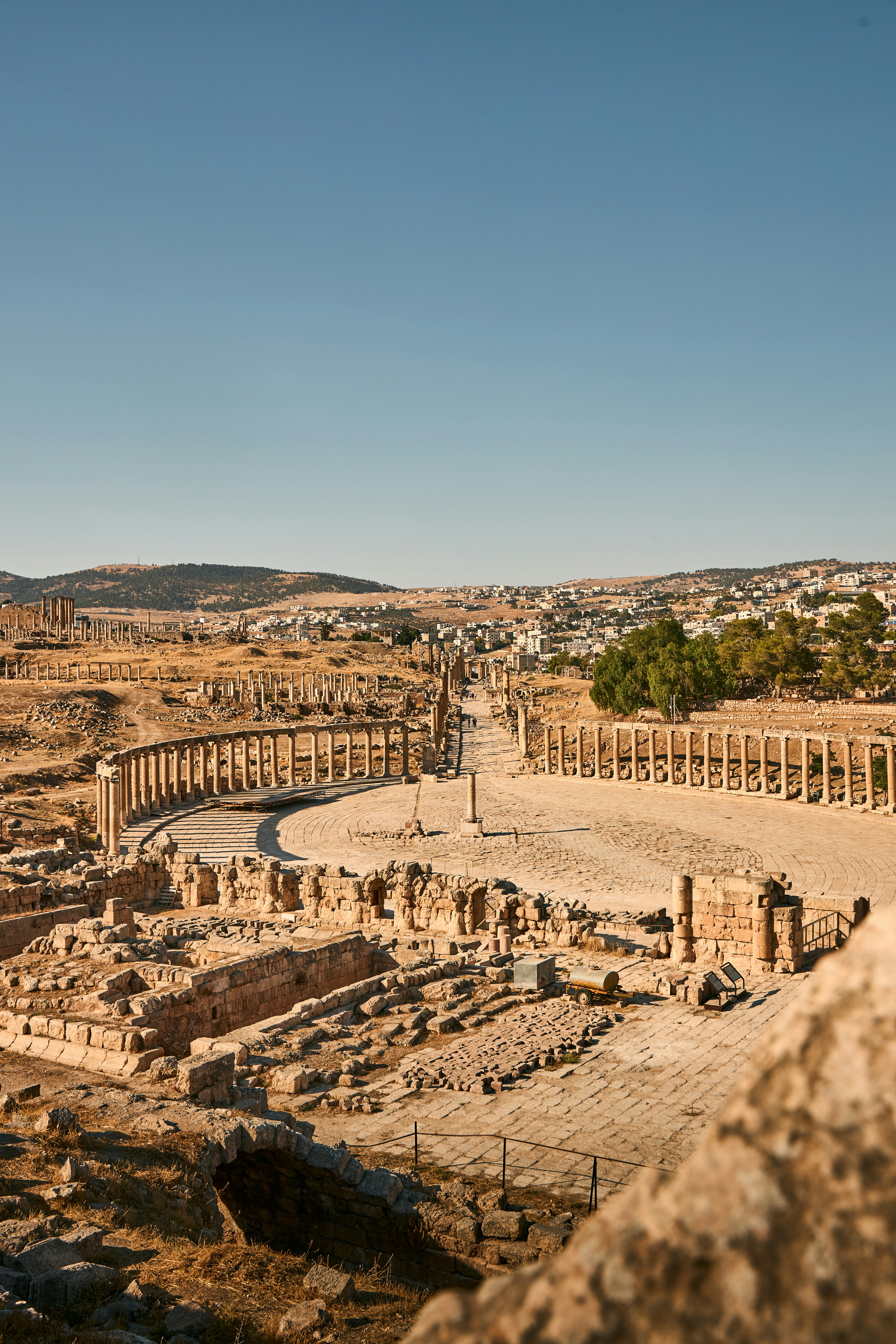 Expansive view of the ancient Roman ruins in Jerash, showcasing the grand colonnade and surrounding landscape under a clear blue sky.