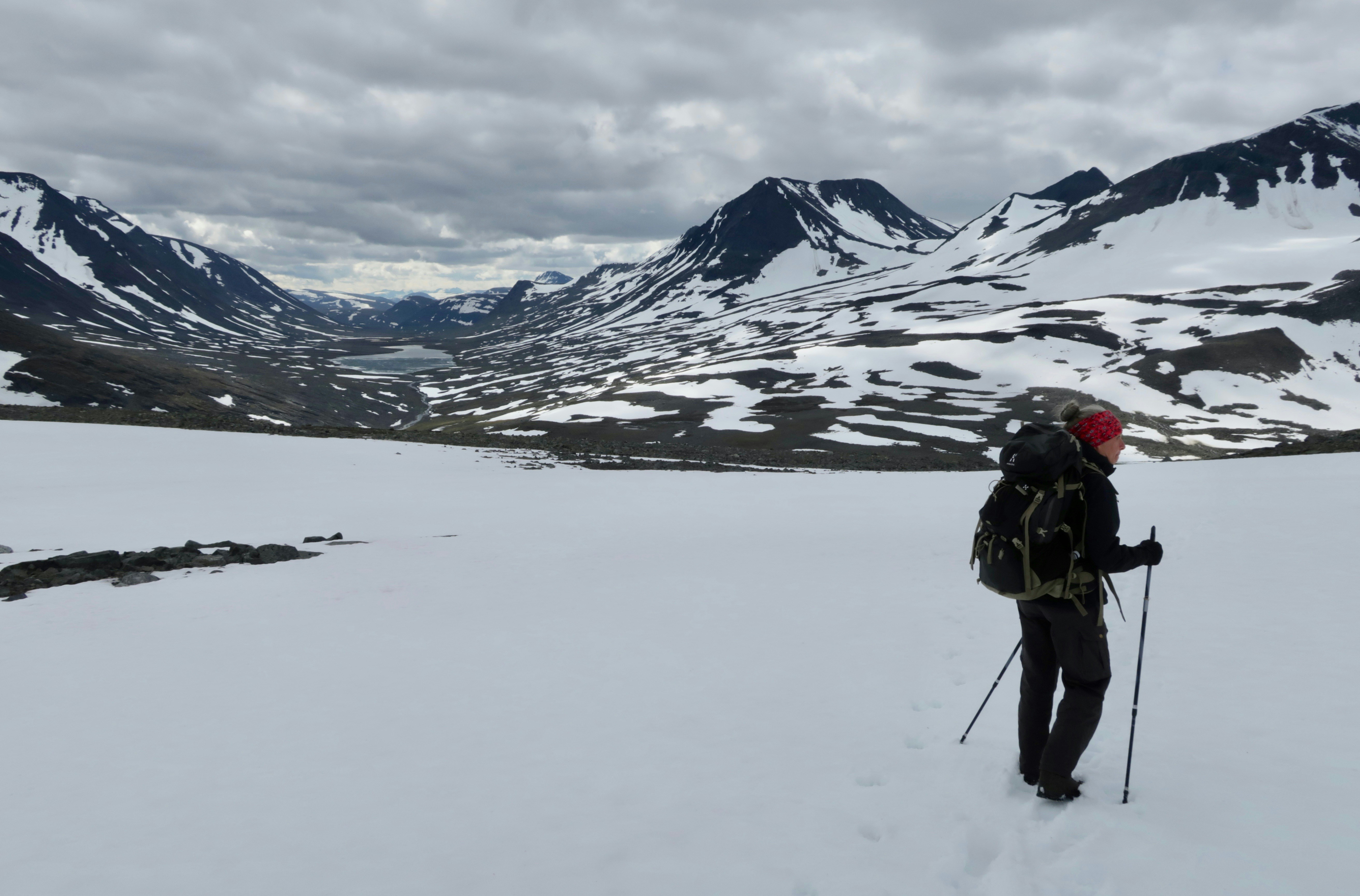 Hiker navigating a snow-covered landscape with towering mountains in the background. The scene captures the essence of adventure and exploration in a remote wilderness.