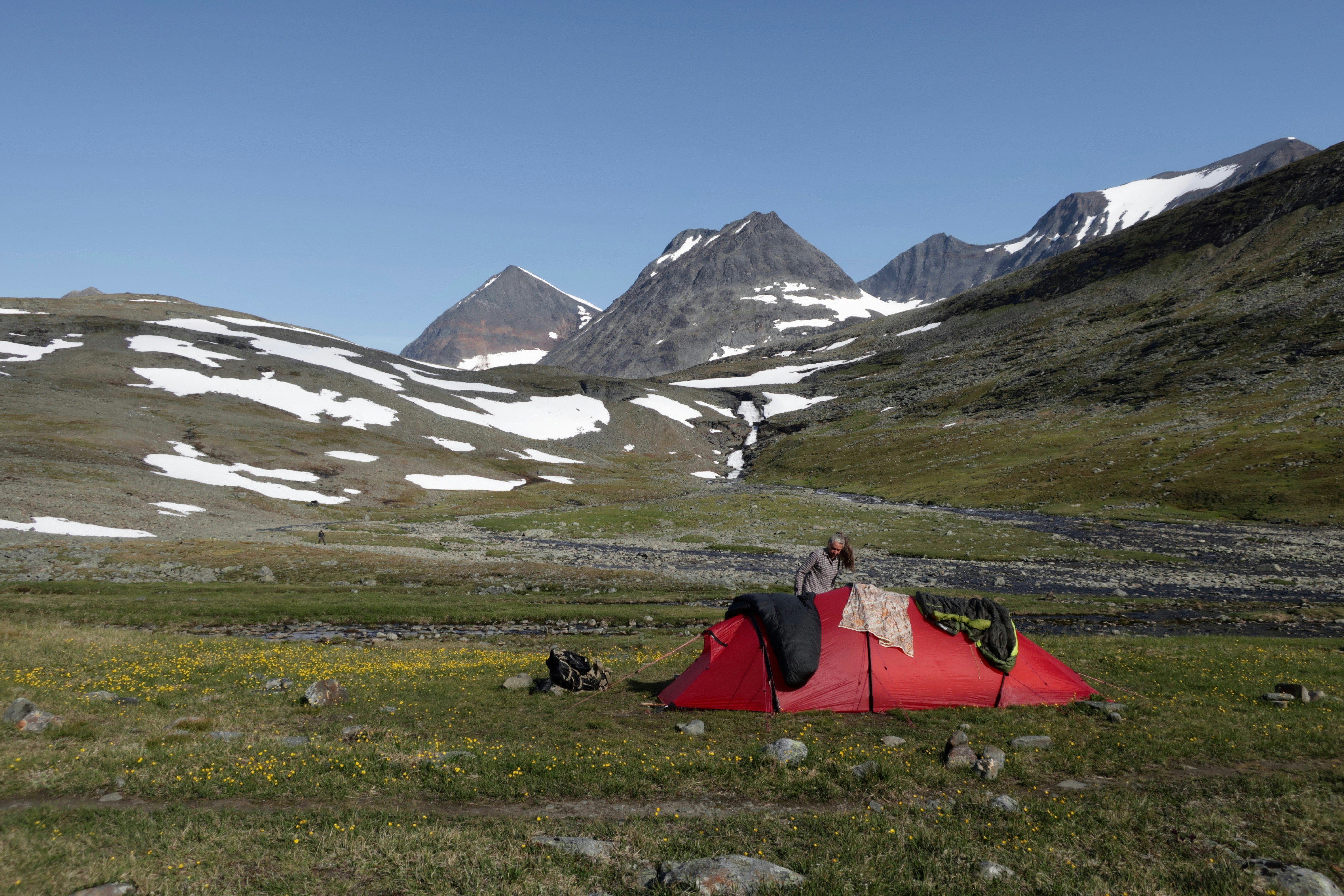 A man standing next to a red tent in the mountains photo – Free Nallo ...