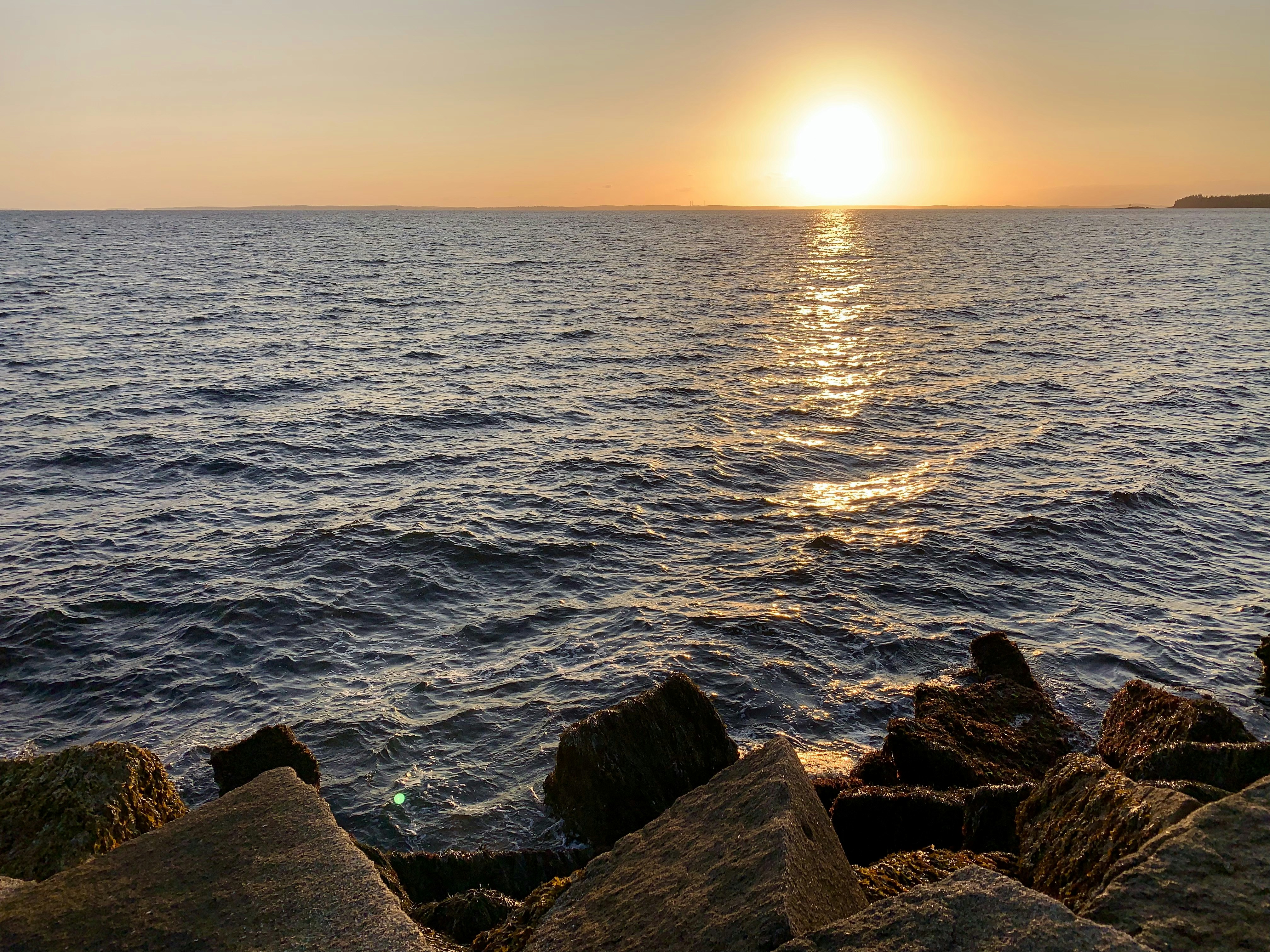 Sunset casting a warm glow over the ocean with rugged rocks in the foreground.