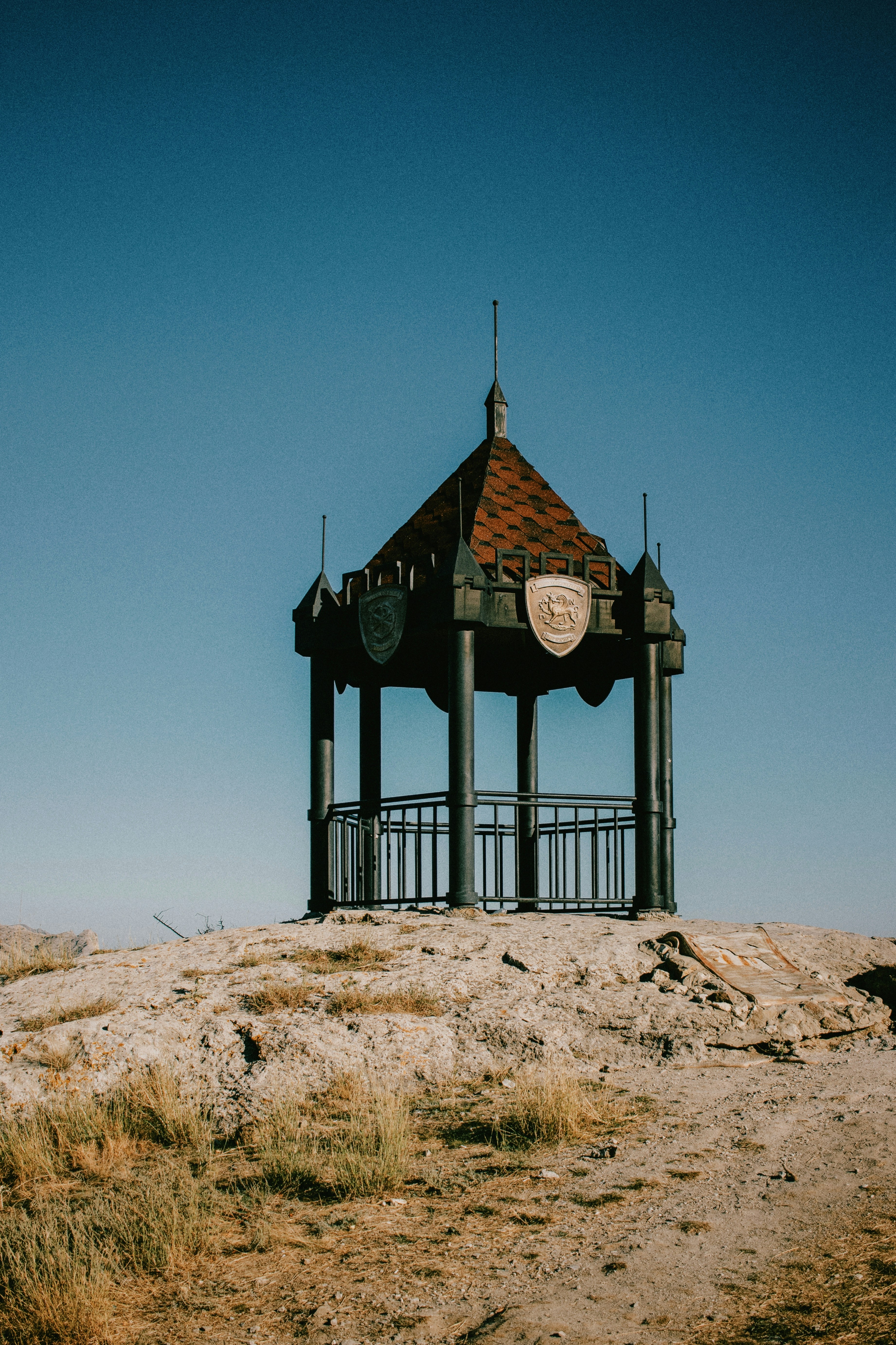 A charming gazebo perched atop a hill, surrounded by sparse vegetation and a clear blue sky.
