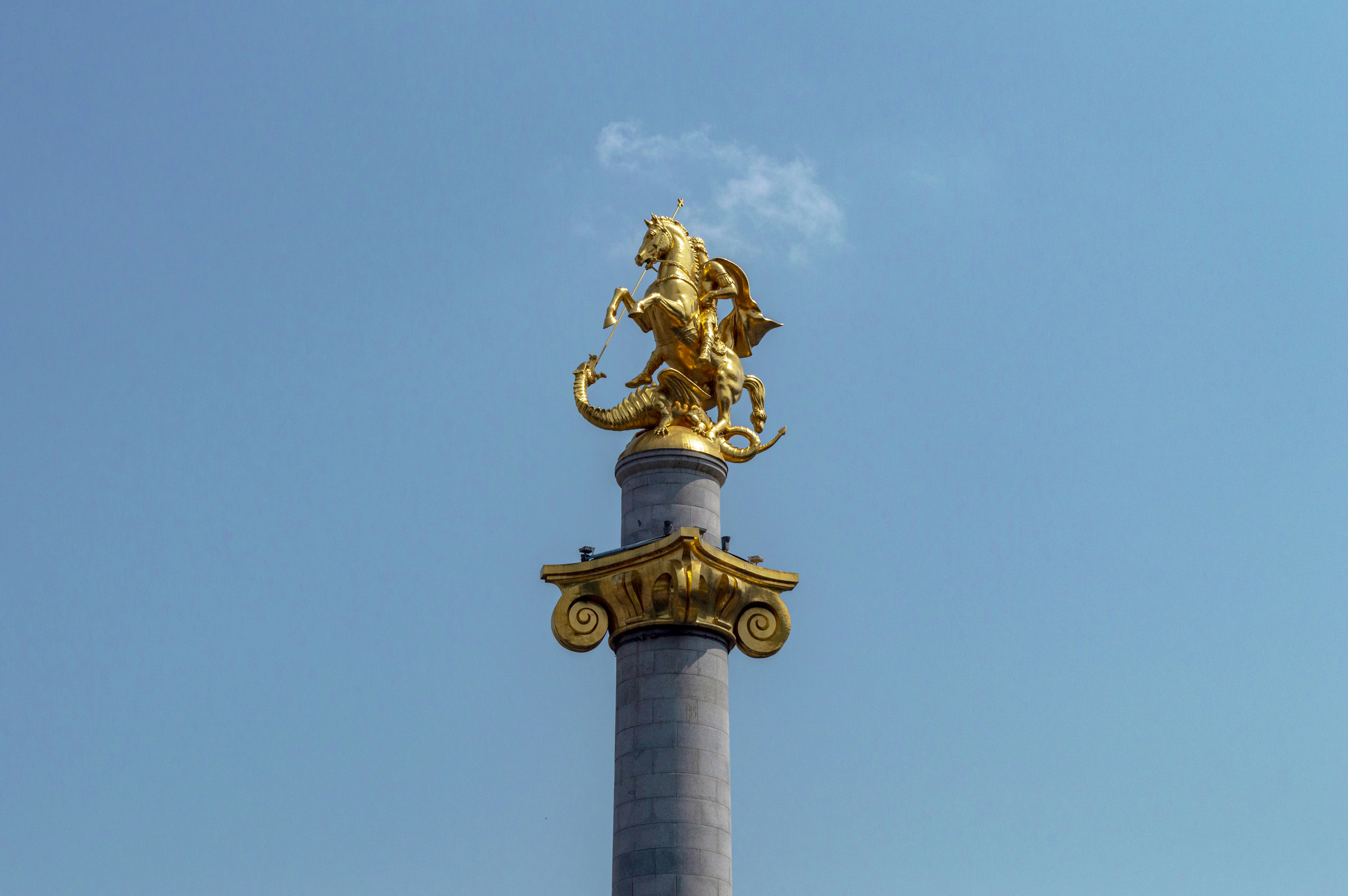 Golden statue of a mythical creature atop a tall column against a clear blue sky.