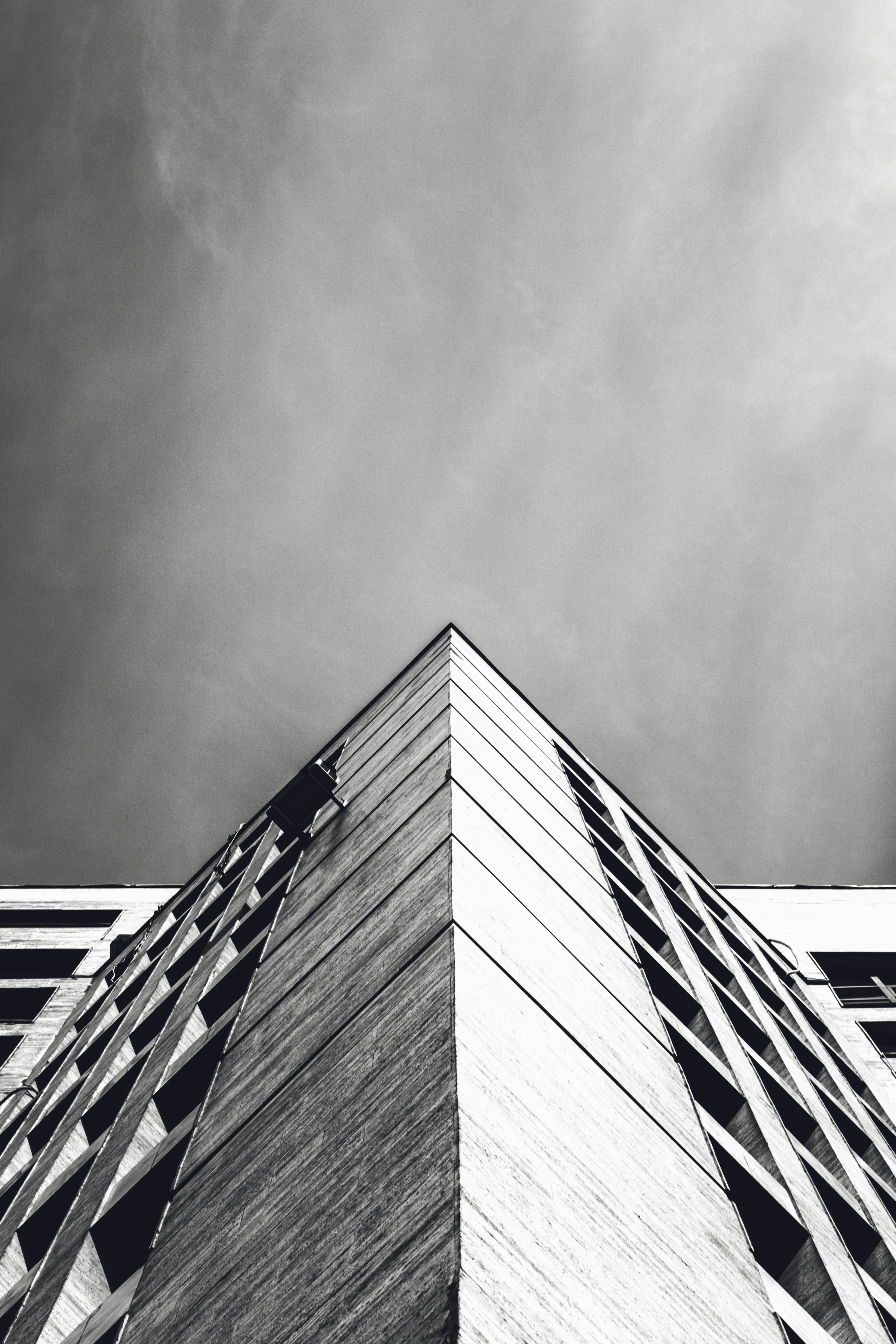 A monochromatic view of a towering building, emphasizing its sharp lines and geometric patterns against a cloudy sky.