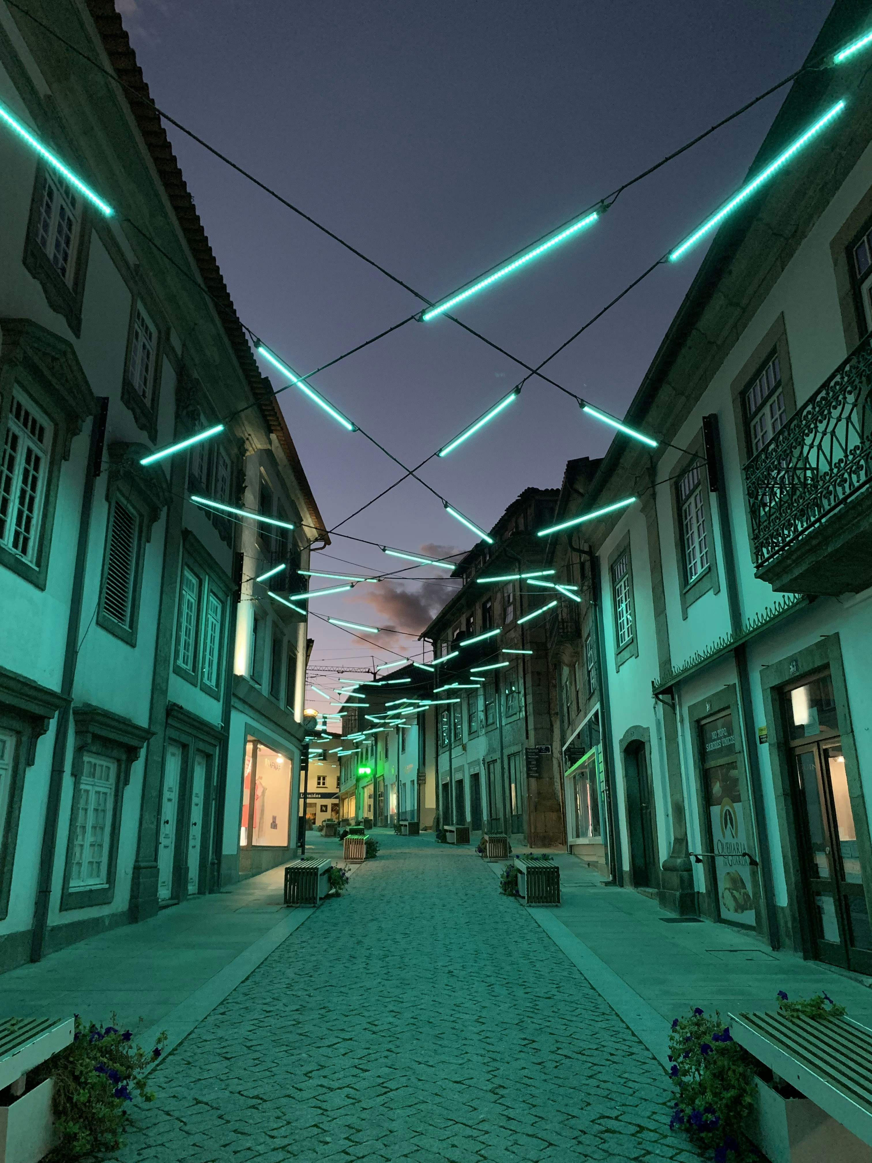 Turquoise Neon Canopy Over a Quiet Cobblestone Street at Dusk