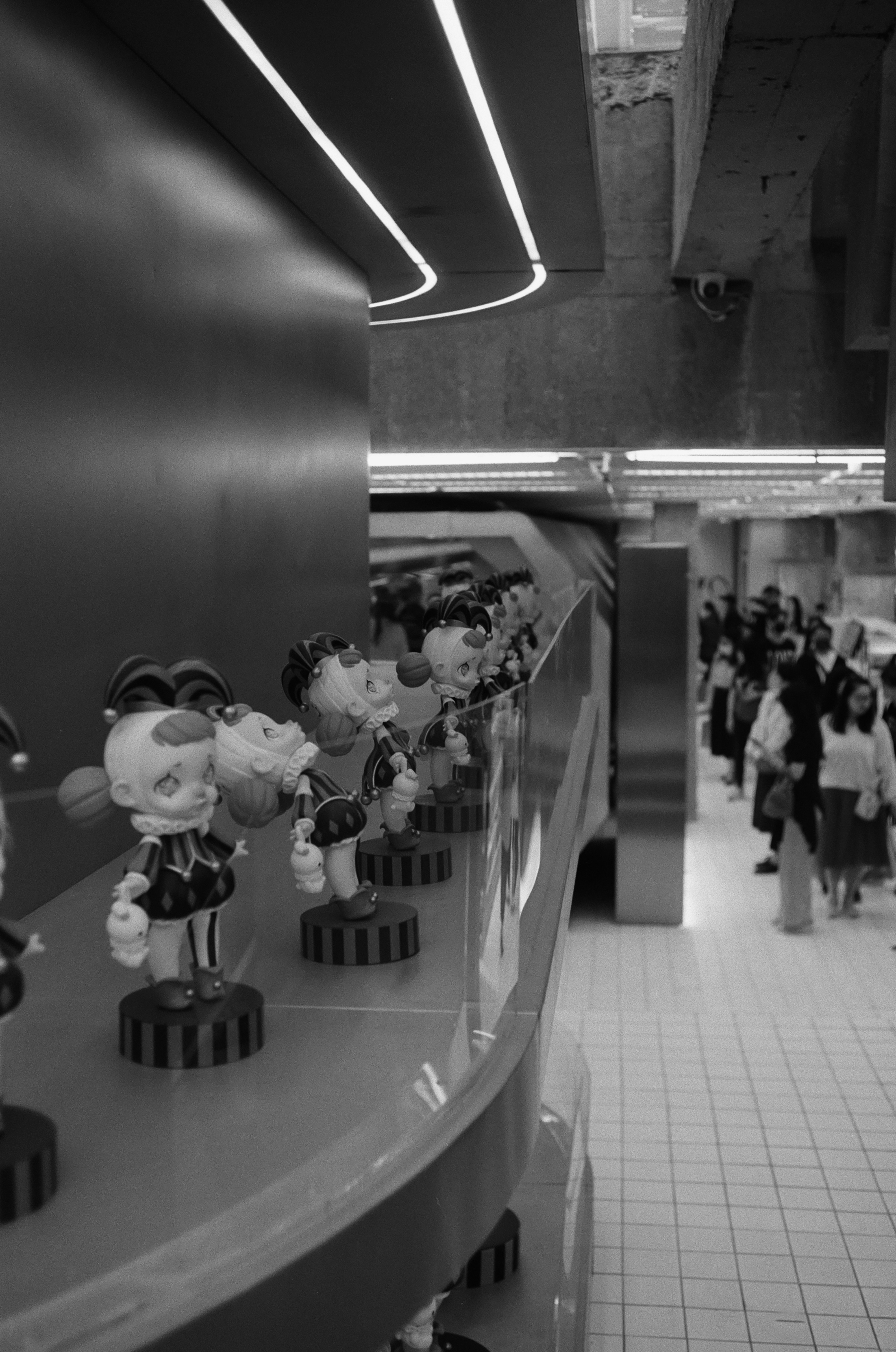 A row of playful figurines displayed in a contemporary setting, with shoppers visible in the background. The scene captures a blend of art and commerce.