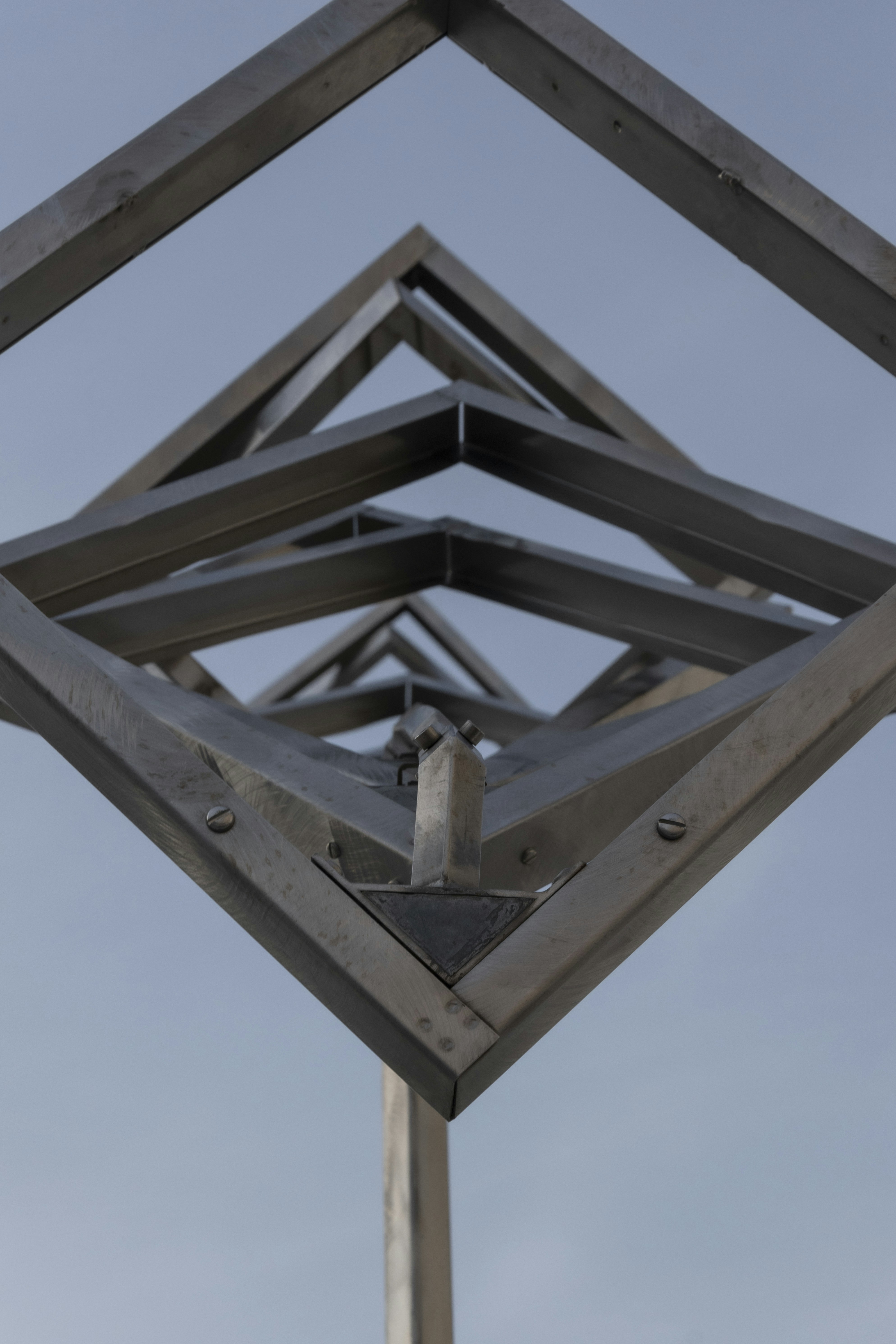 Abstract steel structure converging towards the sky, emphasizing geometric shapes and lines. The composition highlights the interplay of light and shadow.