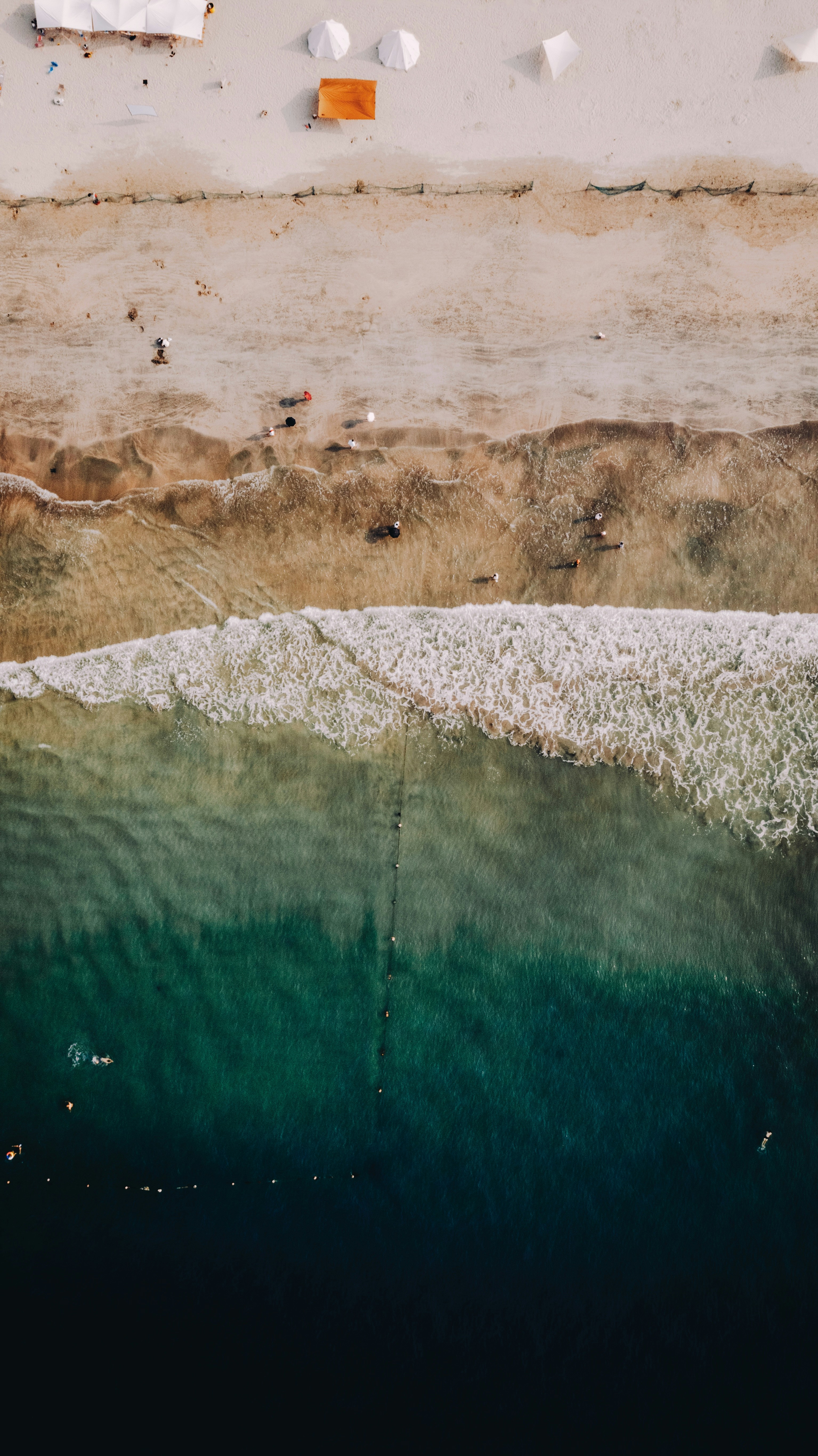 Aerial view of a tranquil beach with sunbathers and colorful umbrellas, where the turquoise waves gently kiss the sandy shore.