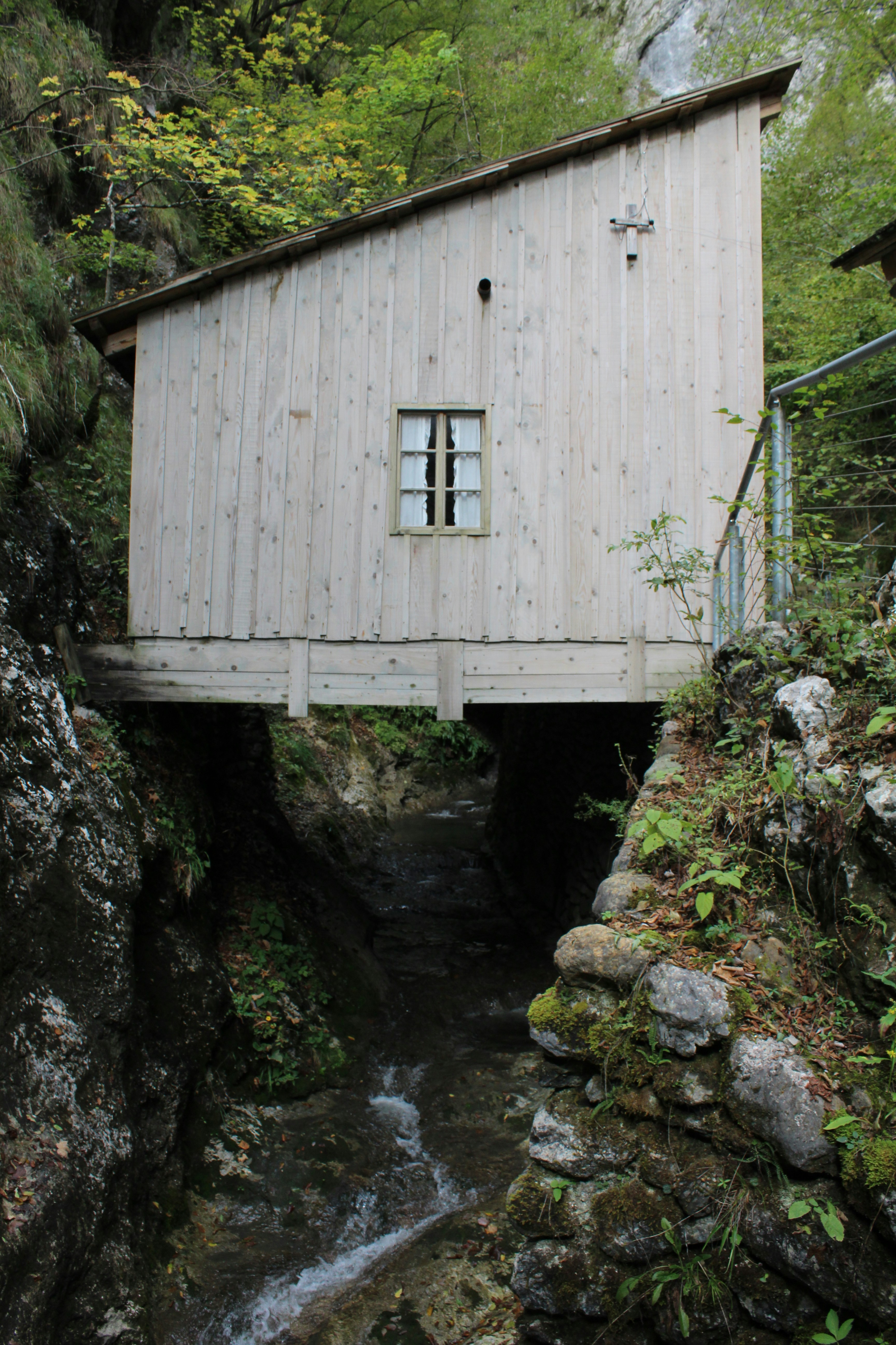 A wooden structure perched above a flowing stream, surrounded by lush greenery in a rocky gorge.
