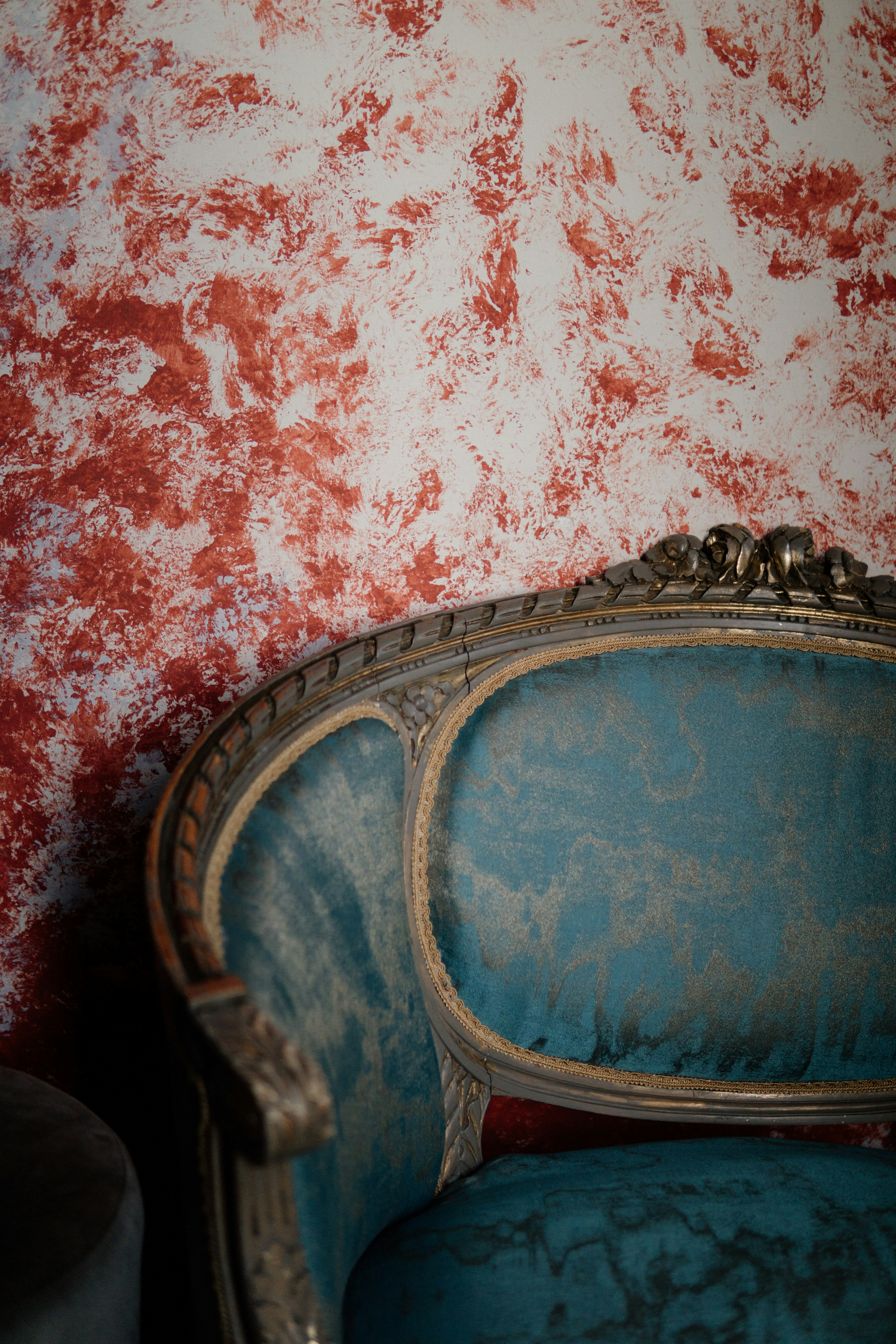 A close-up view of an ornate vintage chair against a textured red and white wall, showcasing its intricate details and faded elegance.
