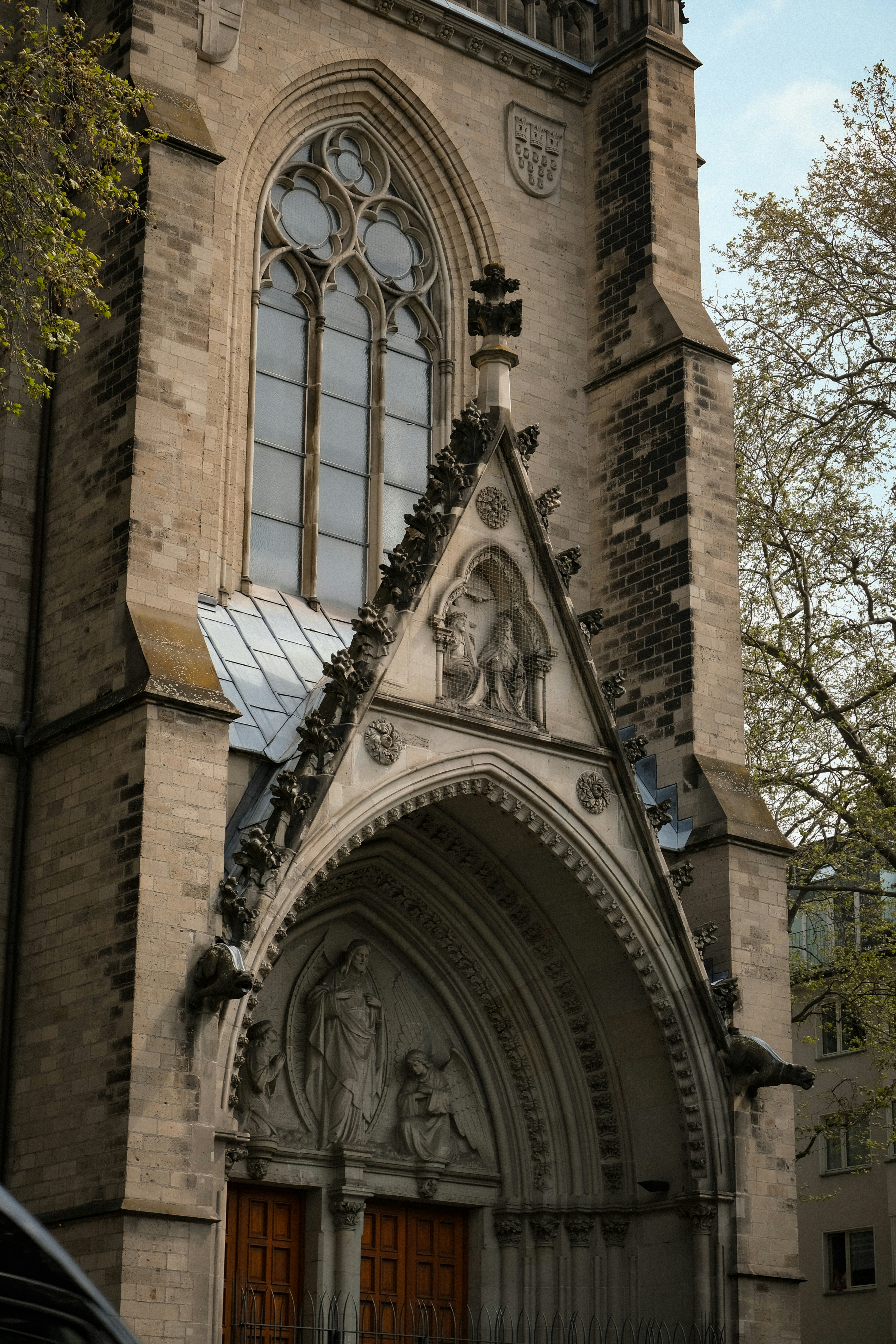Intricate stone carvings adorn the entrance of a historic church, showcasing detailed figures and architectural beauty against a backdrop of trees.